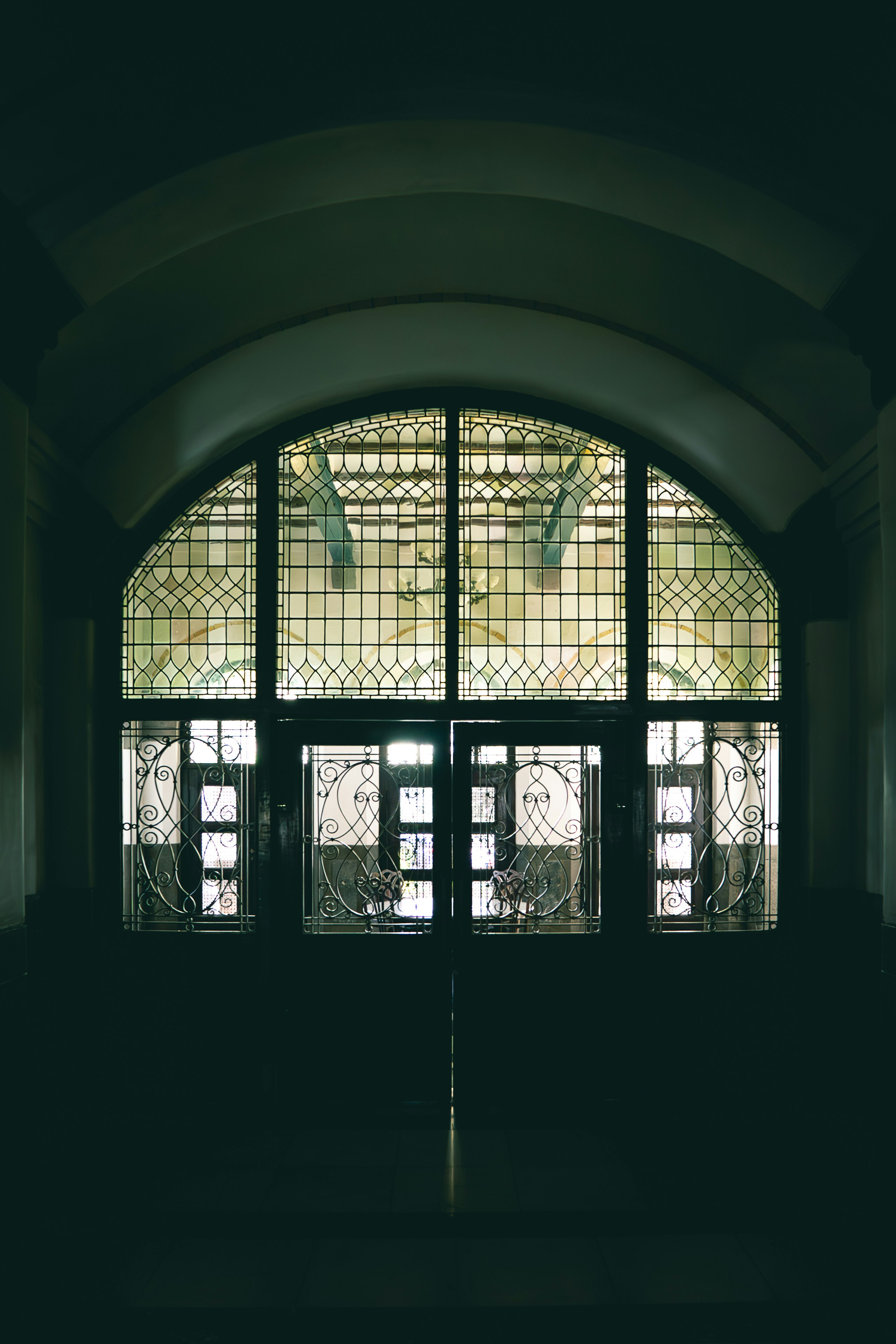 Intricate stained glass doors framed by an arched ceiling, inviting viewers into a softly lit interior space.