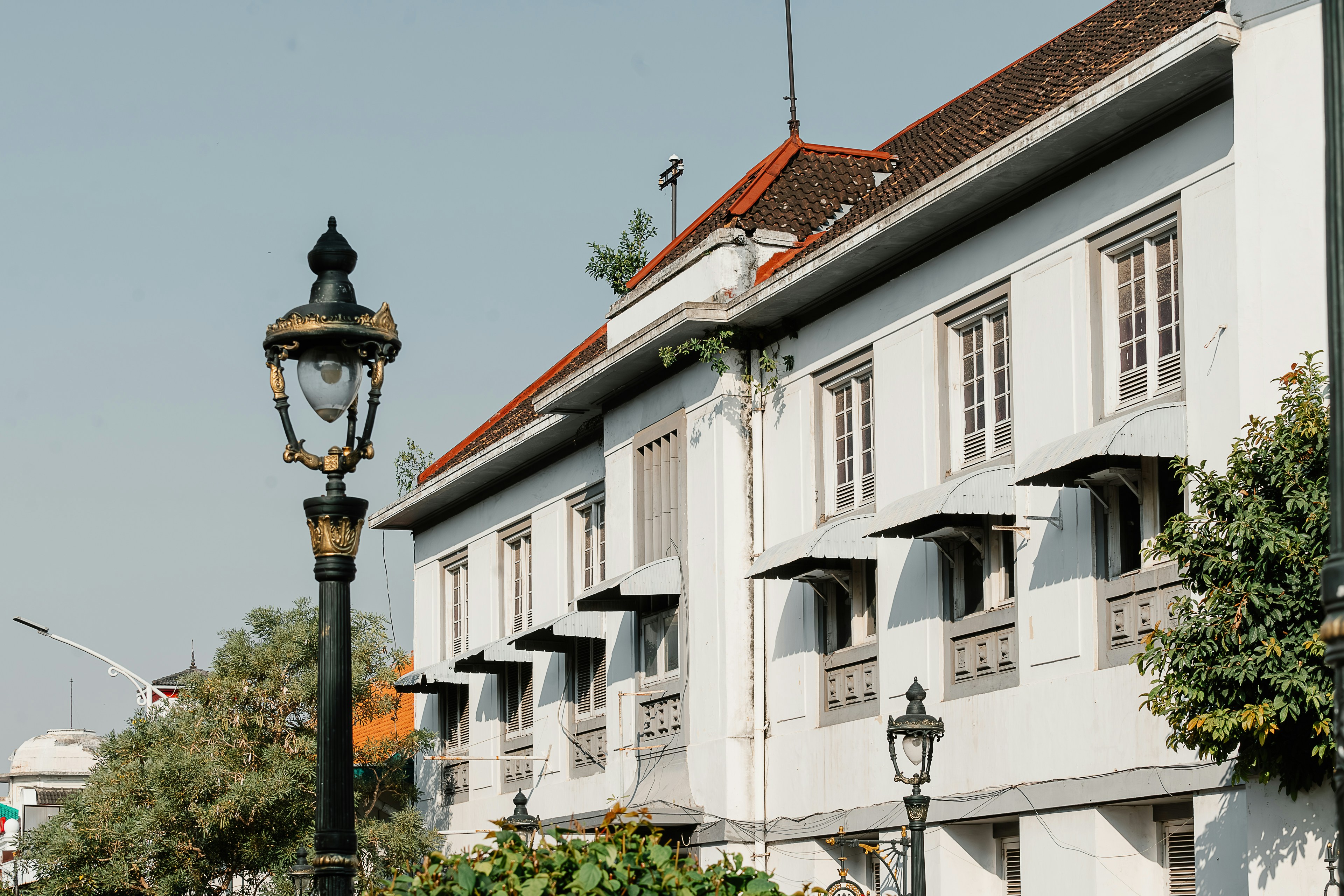 Historic Dutch colonial building with red-tiled roof and ornate street lamps in Semarang under a clear sky.