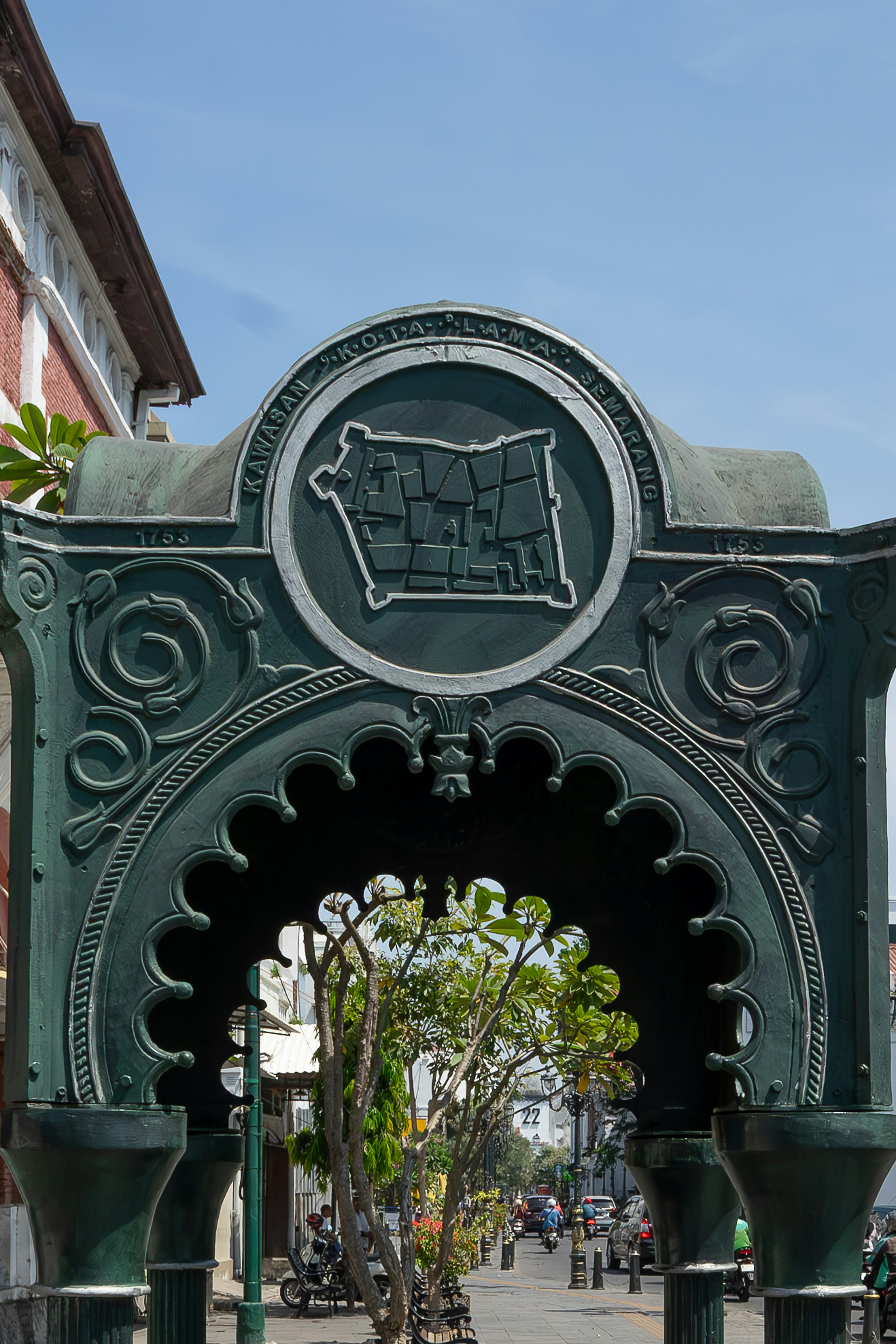 Intricate archway featuring a detailed map emblem, framed by lush greenery and bustling street life.