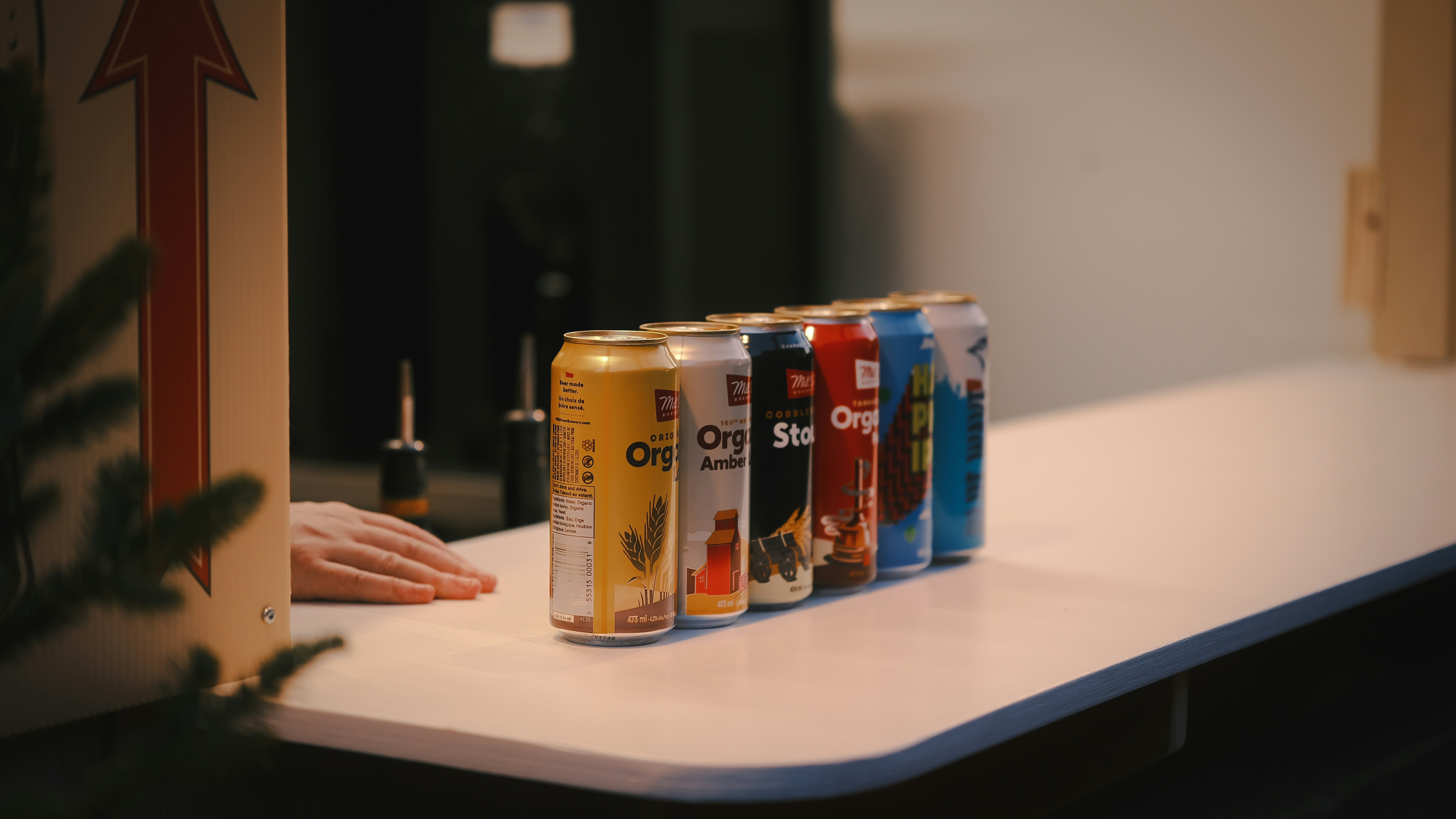 A row of colorful beverage cans displayed on a counter, with a hand resting nearby. The scene captures a casual moment of choice.