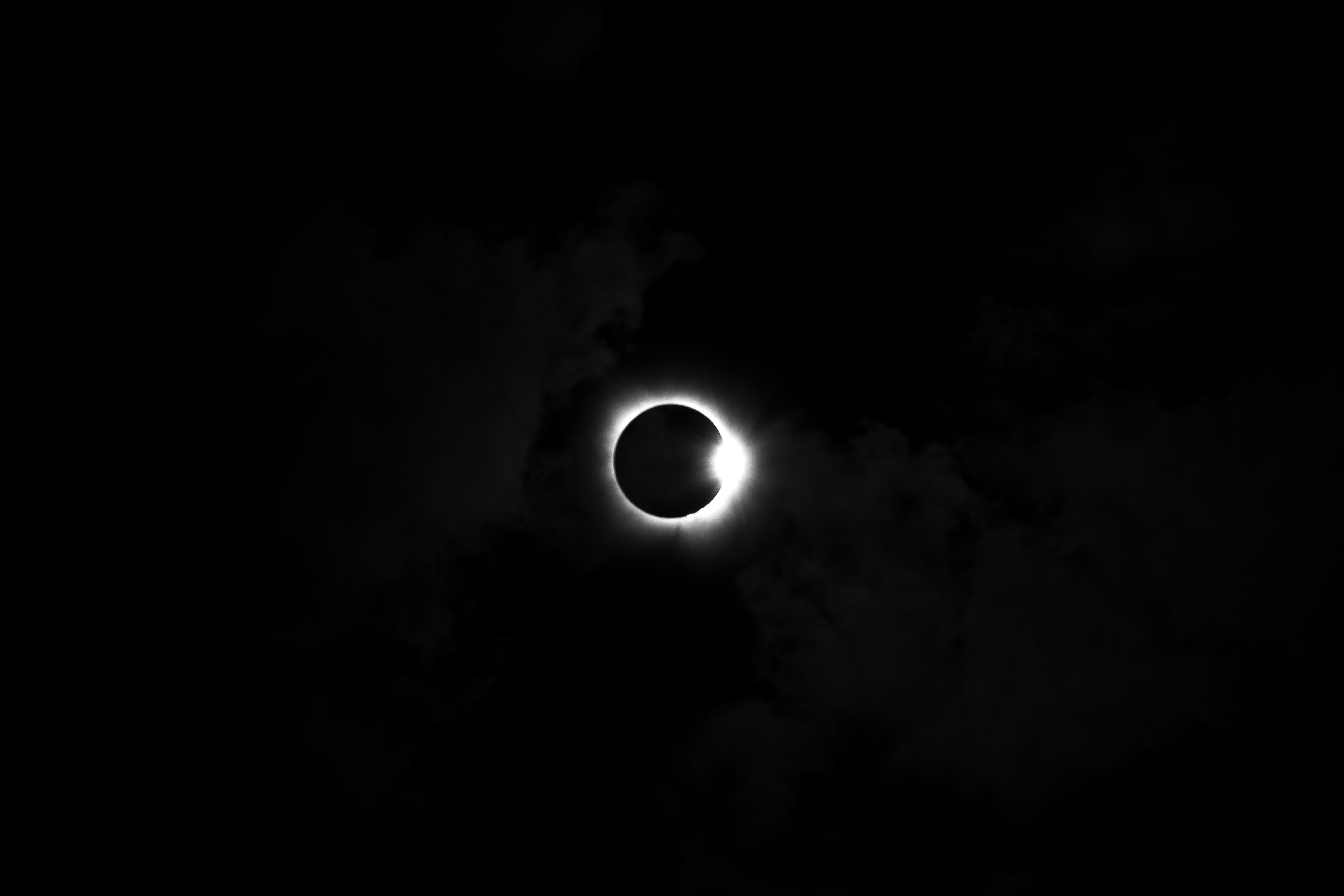Solar eclipse with a luminous corona surrounded by shadowy clouds.