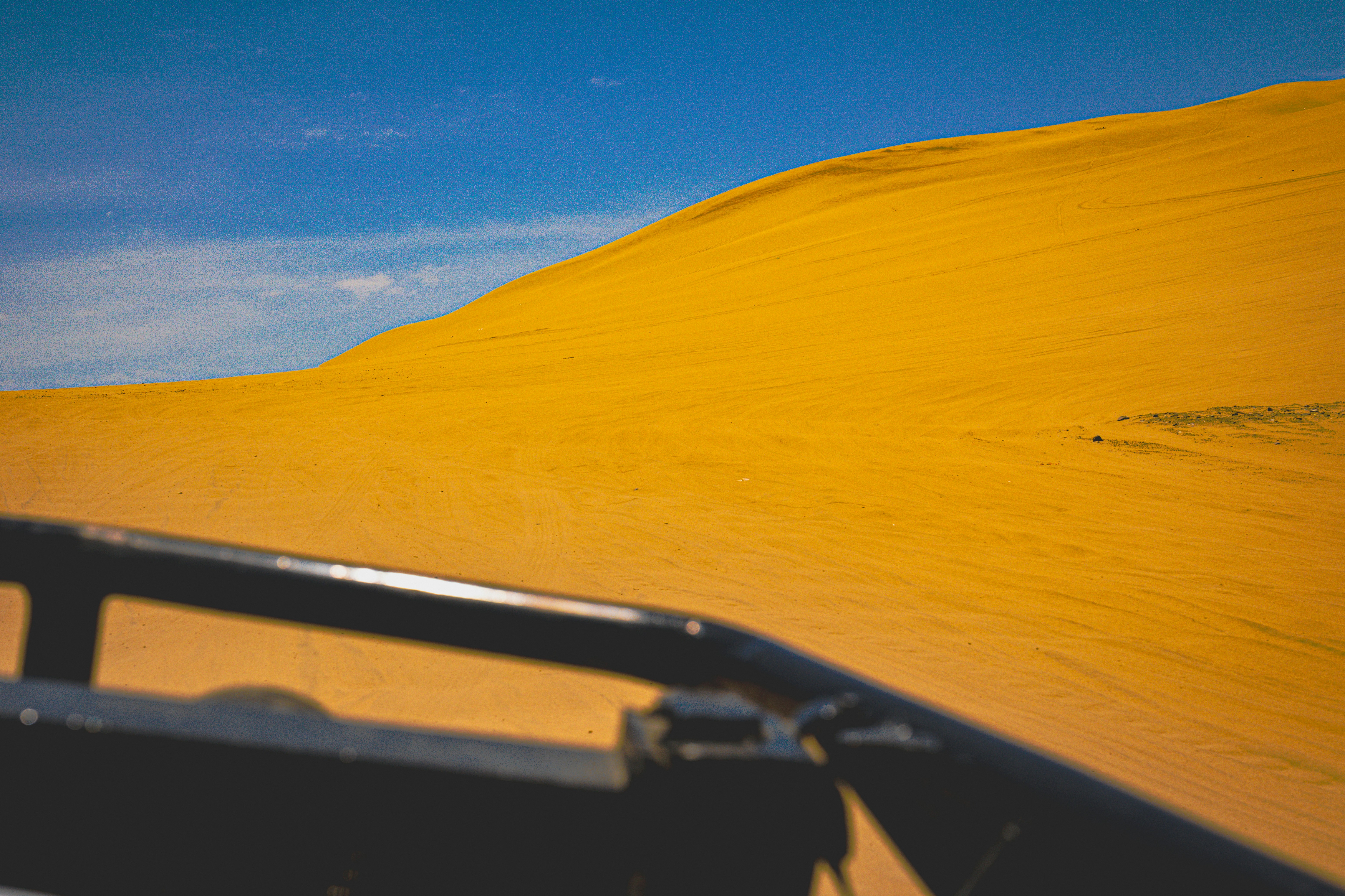 Vast golden sand dune under a clear blue sky, viewed from a vehicle's perspective.
