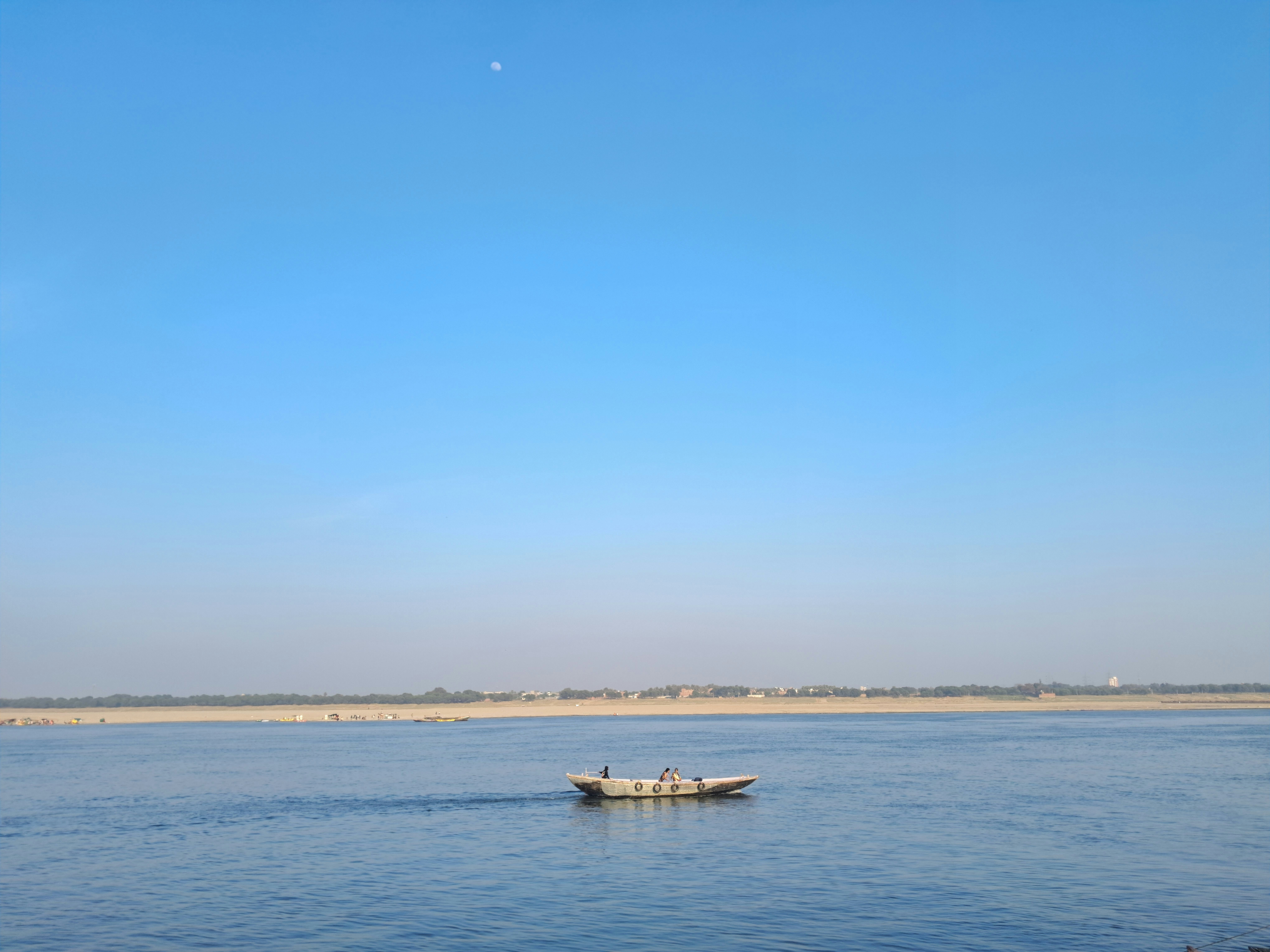 Boat gliding across the Ganges River under a cloudless blue sky.