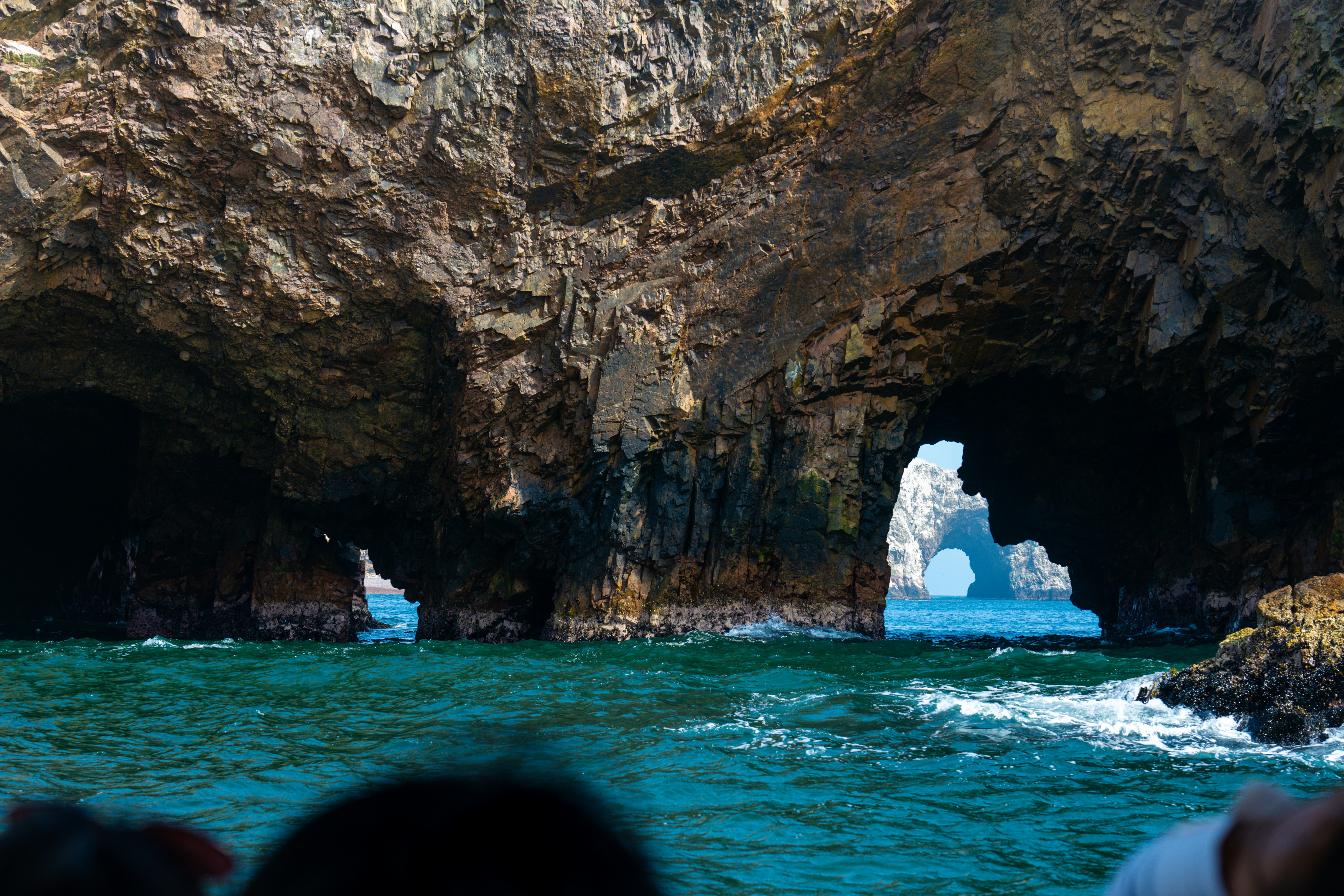 Two natural rock arches frame a vibrant blue sea, creating a striking contrast against the rugged coastline. The scene captures the essence of coastal erosion and natural beauty.