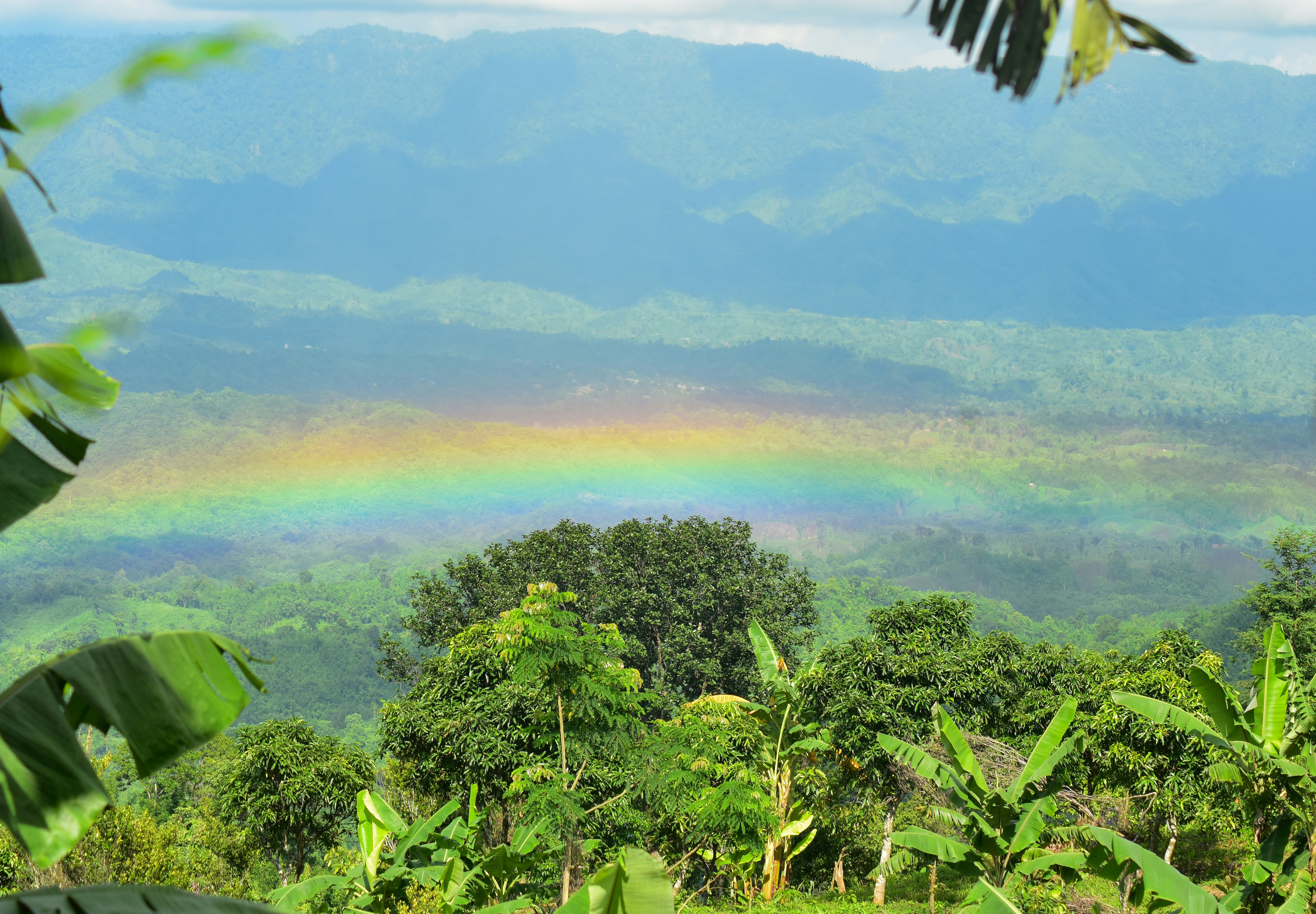 Lush green hills under a vivid rainbow arch with distant mountains.