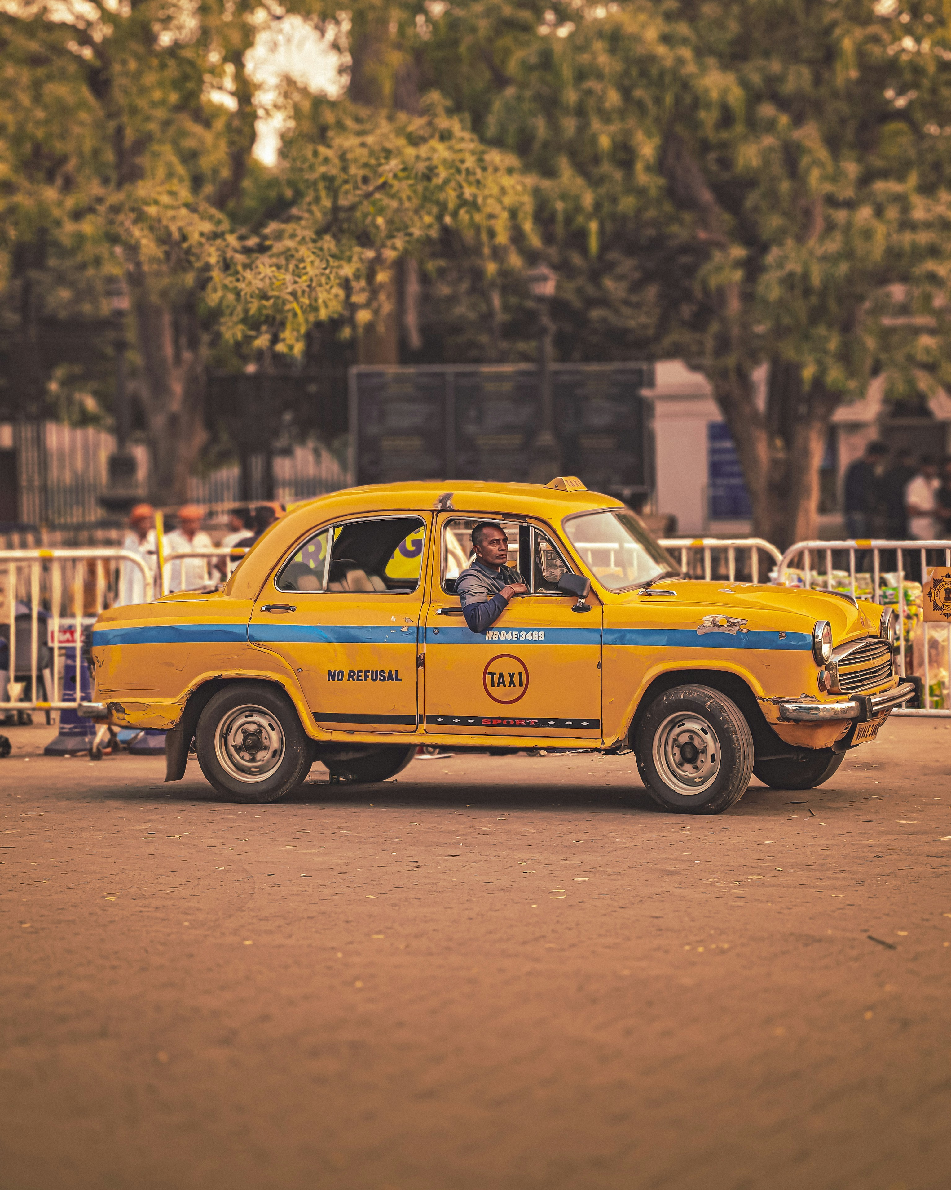A yellow taxi driving down a street next to a fence photo – Free Car ...