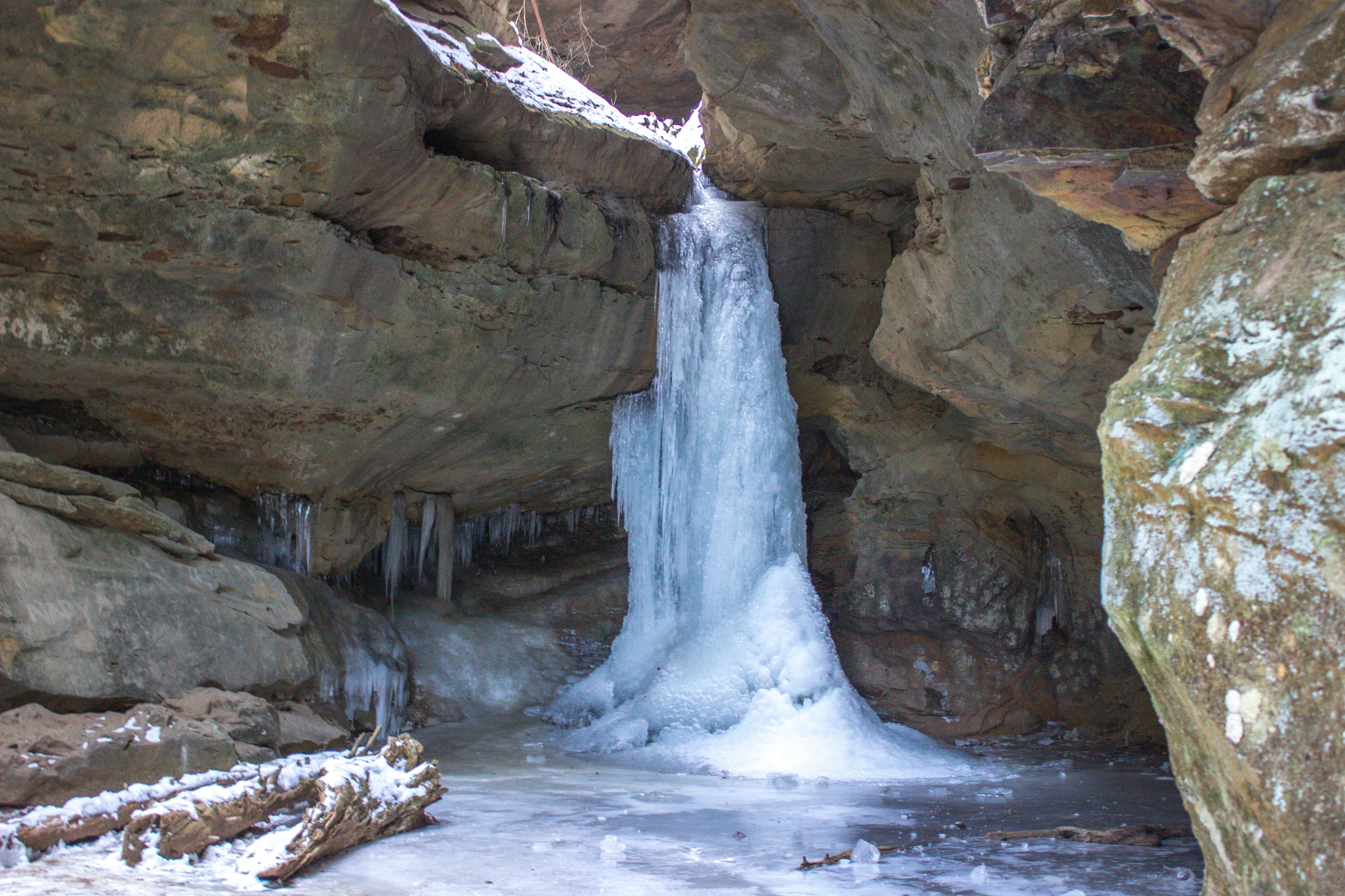 Frozen waterfall cascades between rugged rock formations, surrounded by icicles and a layer of snow.