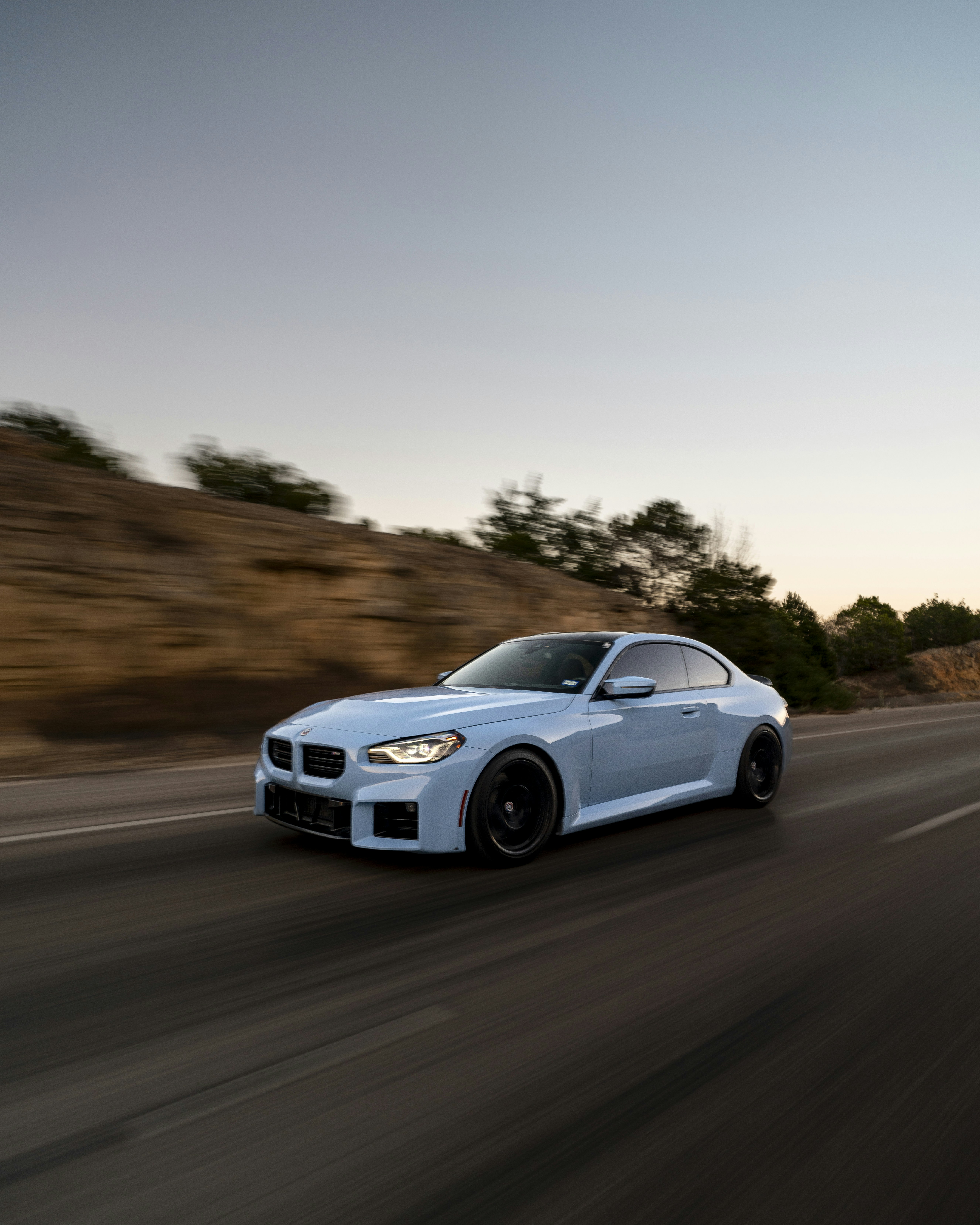 A white car driving down a road next to a hillside photo – Free Bmw ...