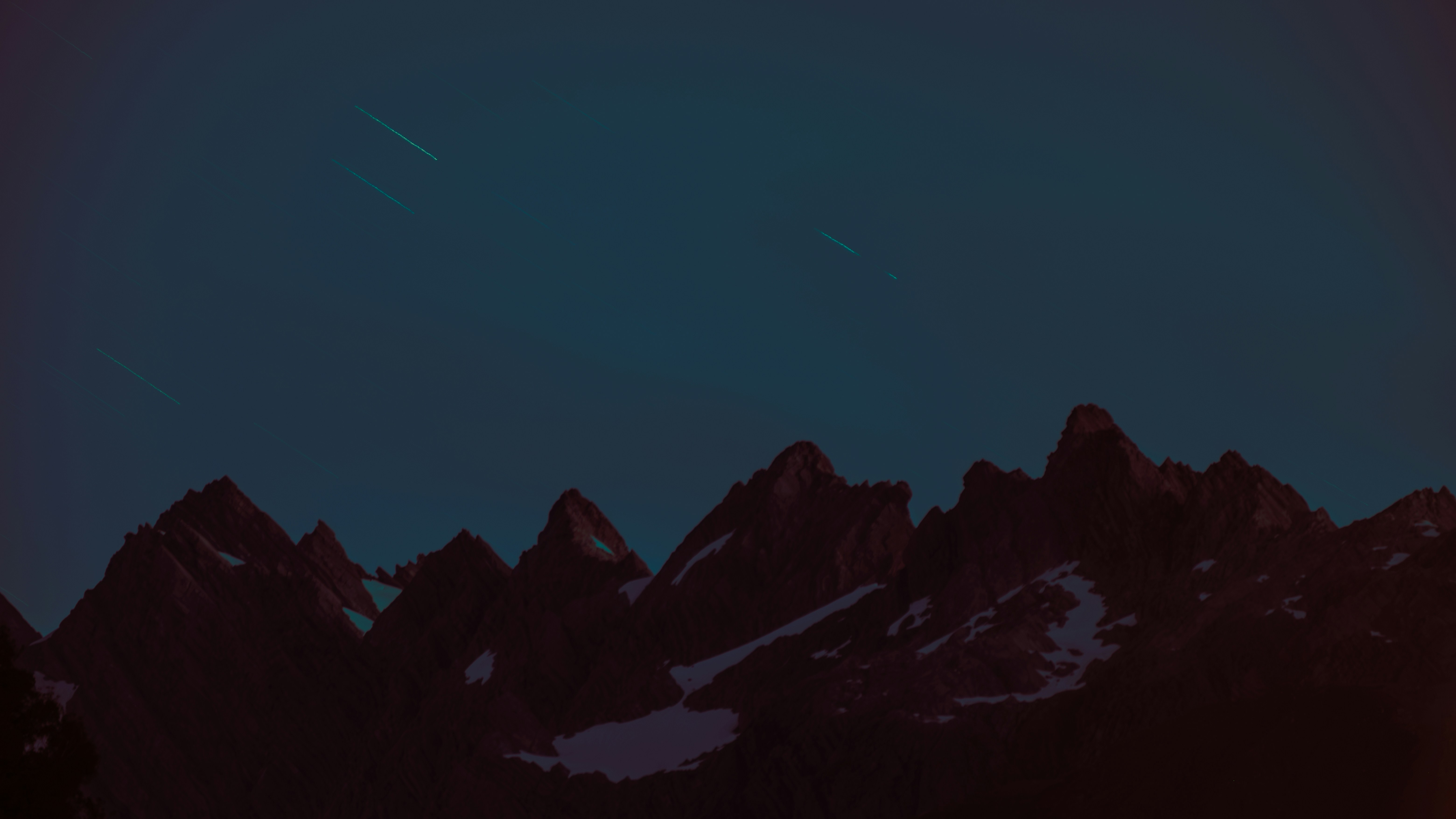 Silhouetted mountain peaks beneath a twilight sky with faint star trails.