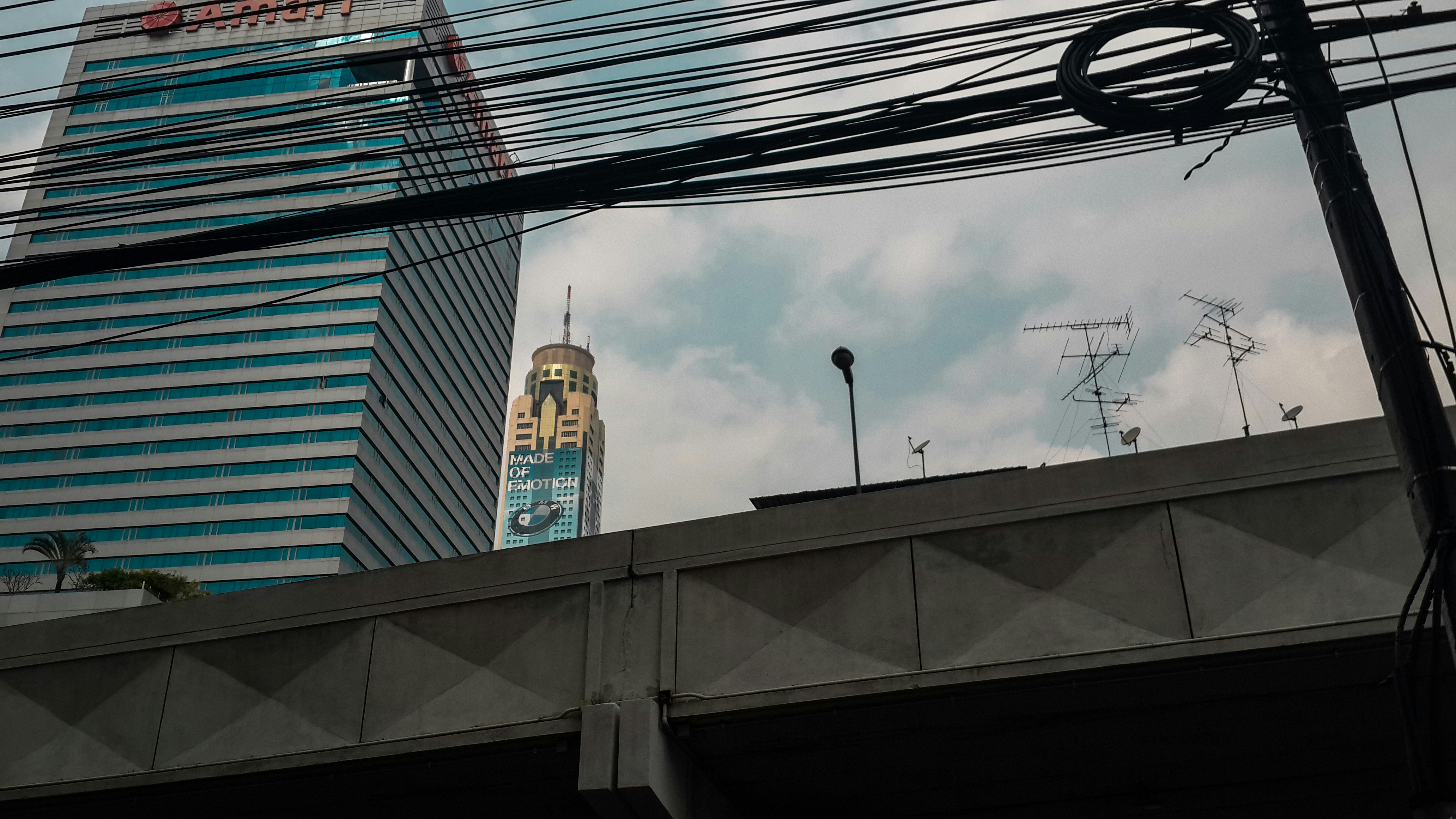 High-rise buildings and tangled wires against a cloudy sky in Bangkok.