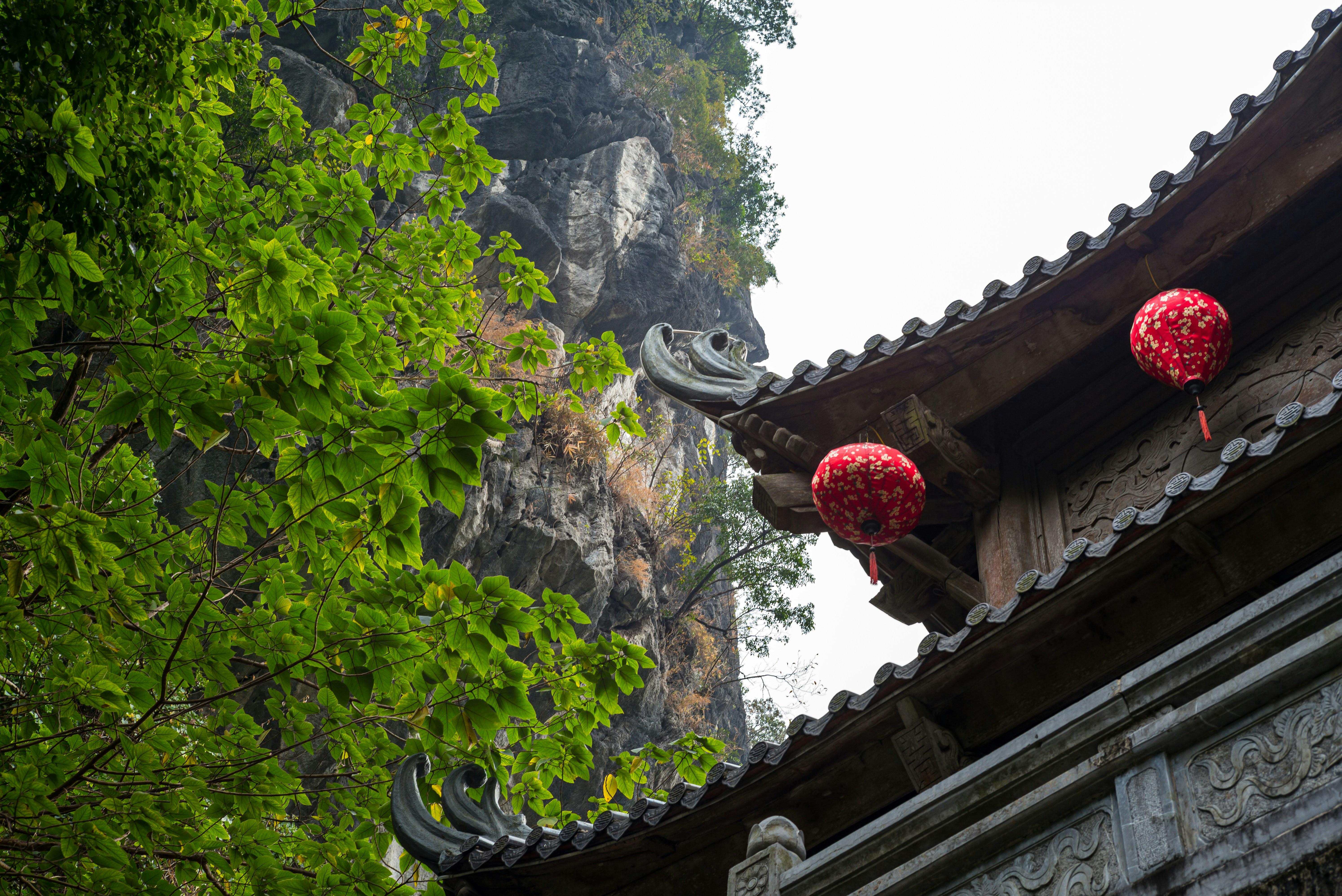 Crimson Lanterns Gracing a Carved Roof Above a Cliffside Shrine