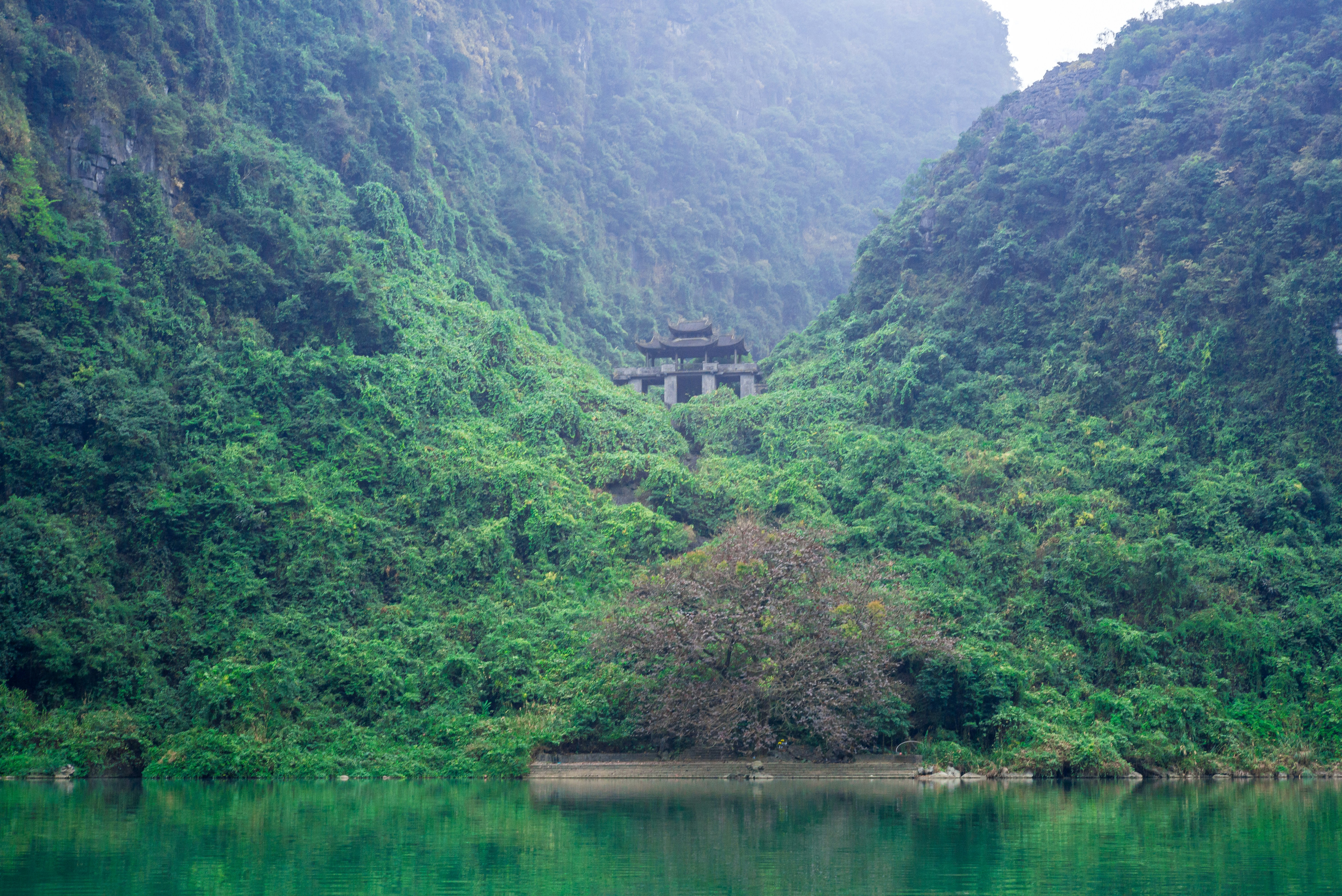 Ancient structure nestled in lush green mountains overlooking a tranquil lake.