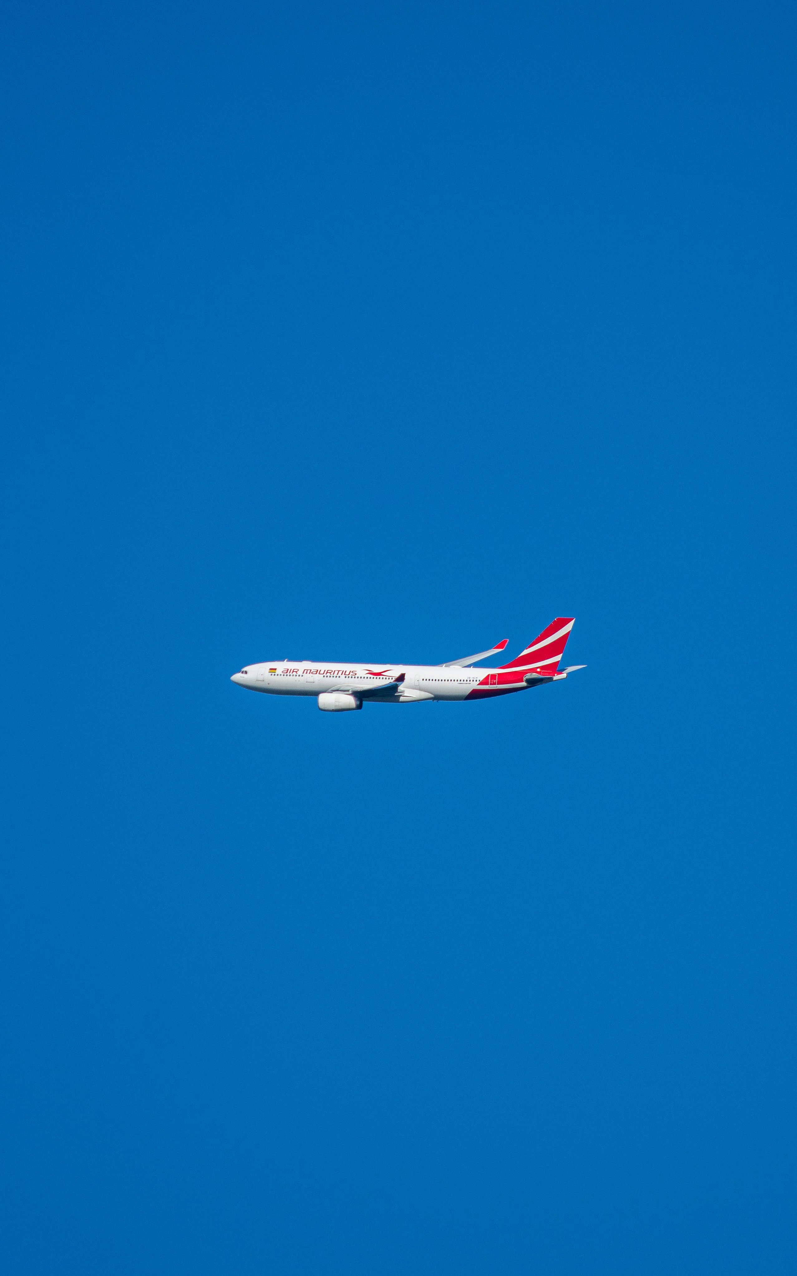 Airplane with red tail soaring through a clear blue sky.