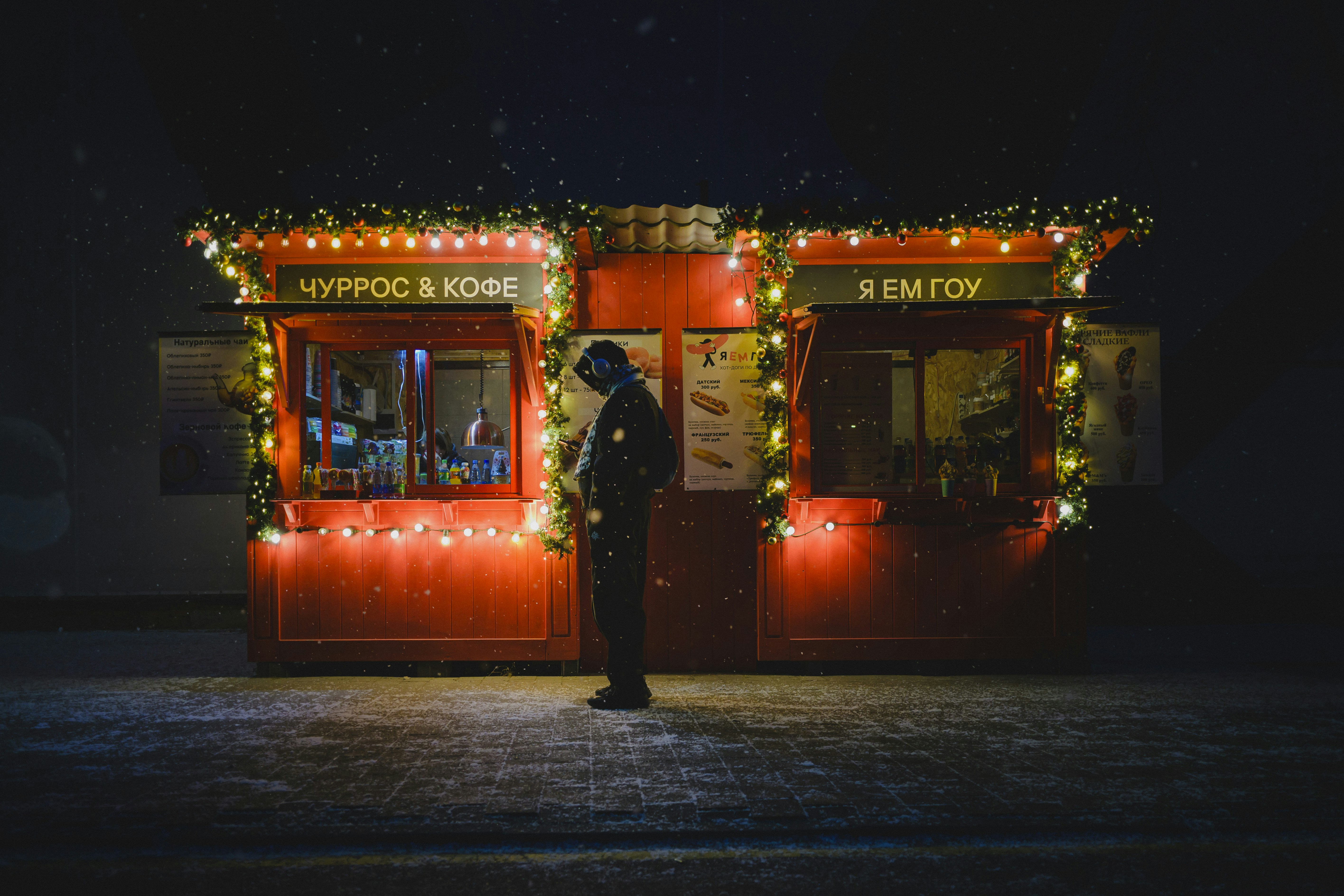 A red street food vendor. | A man standing in front of a building covered in christmas lights