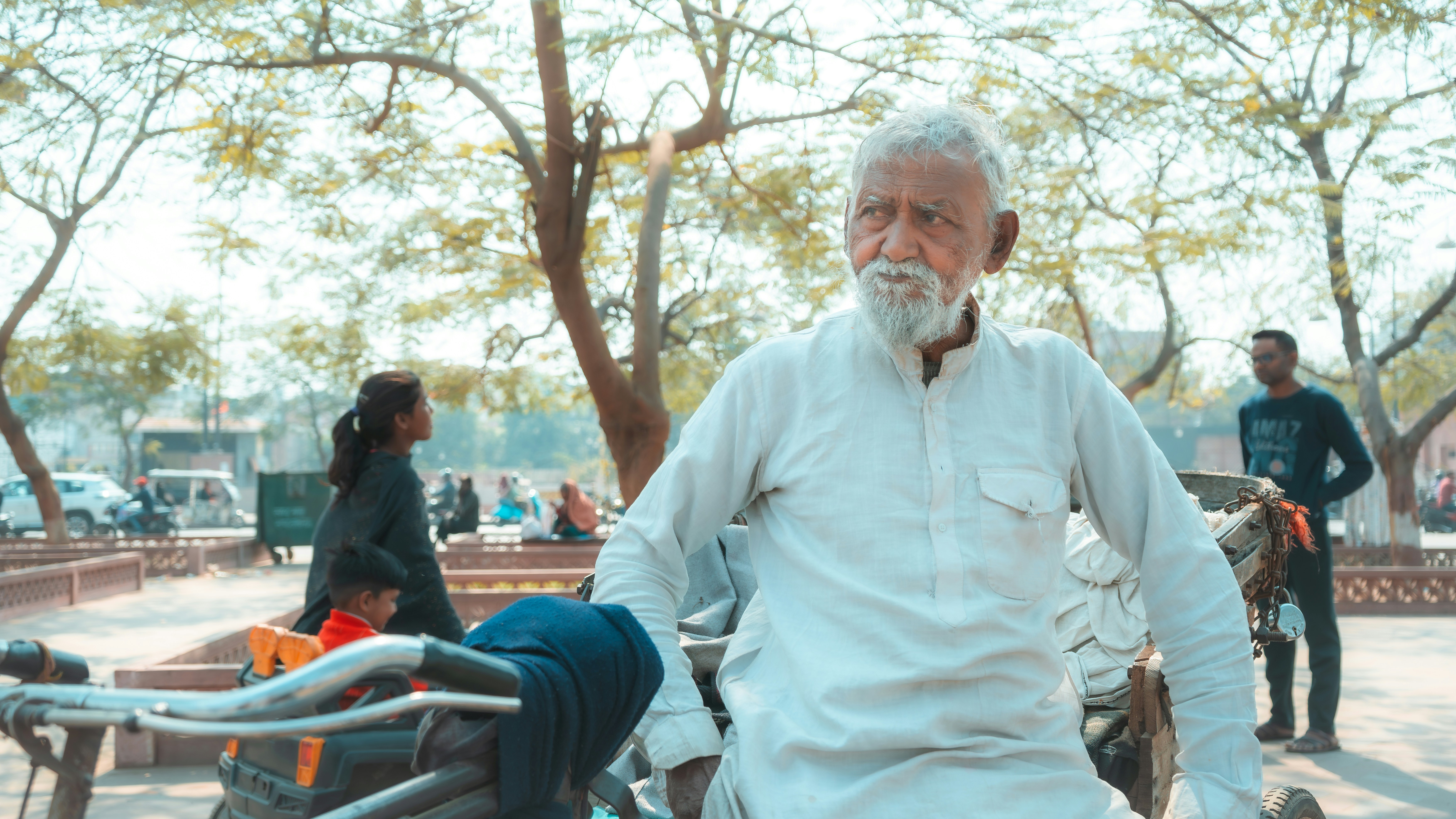 Sunlit Solitude: A White-Clad Elder Beside a Park Rickshaw