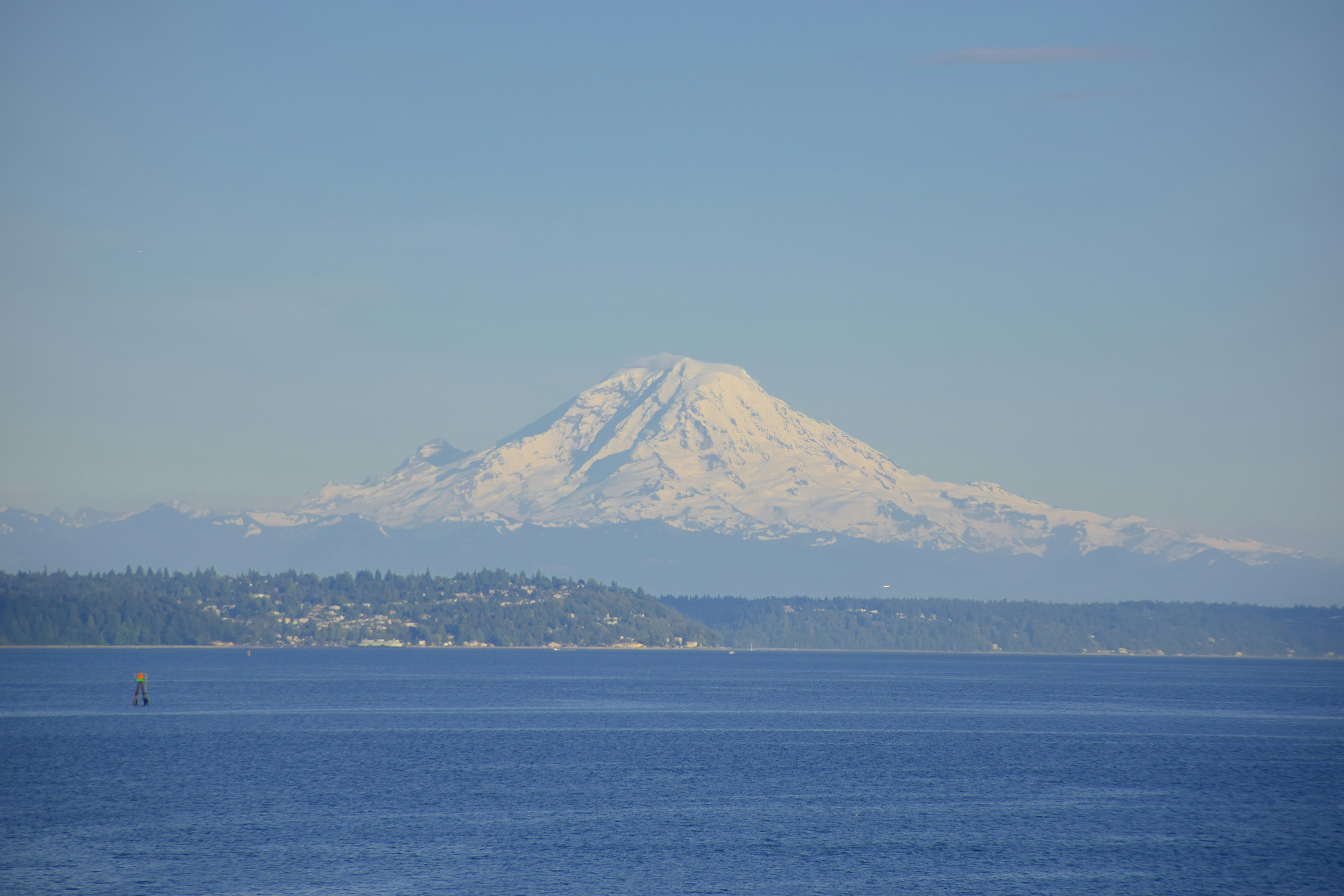 Snow-capped Mount Rainier rising above the blue waters of Puget Sound under a clear sky.