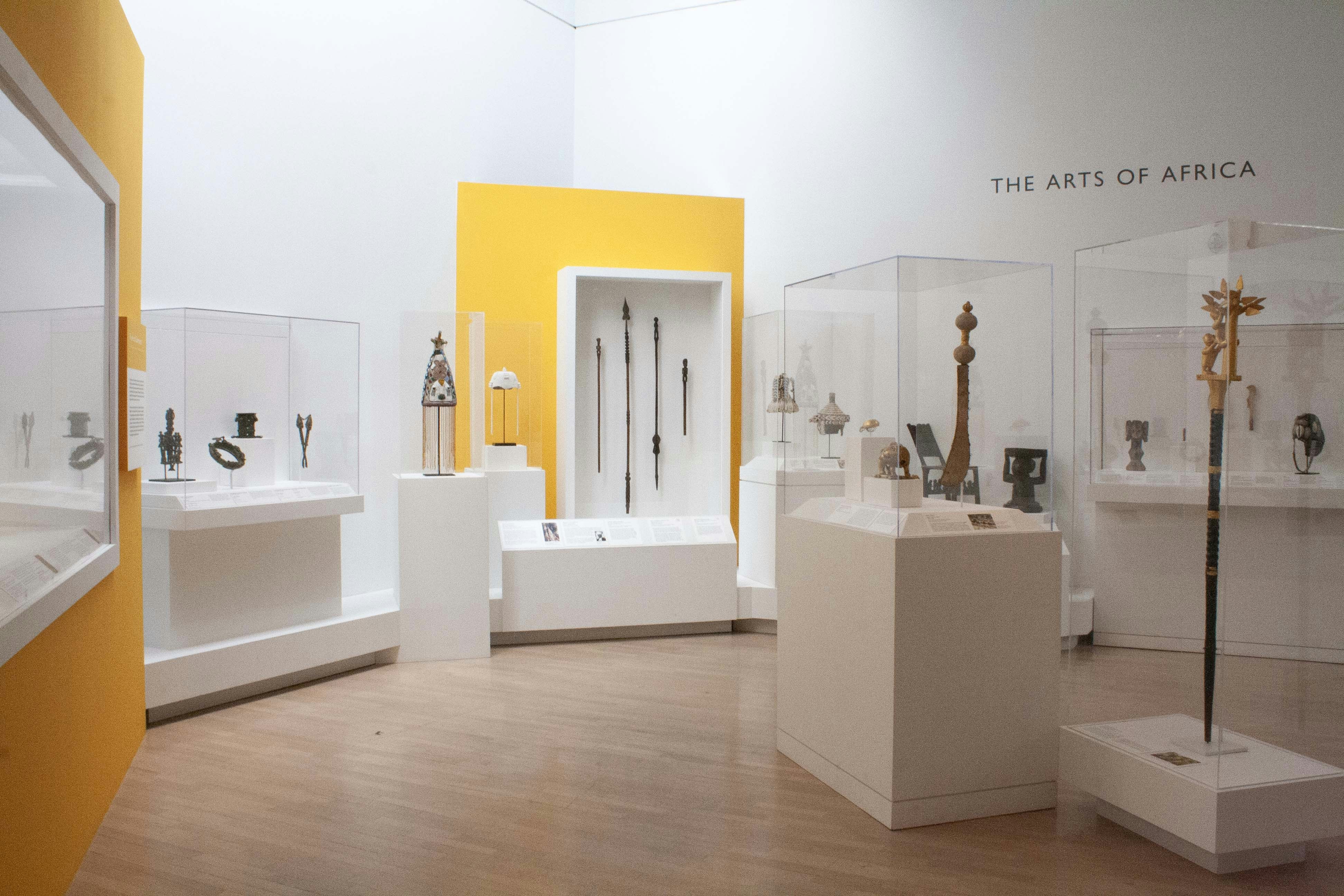 Art gallery exhibit with ancient artifacts displayed in glass cases against a white and yellow backdrop.