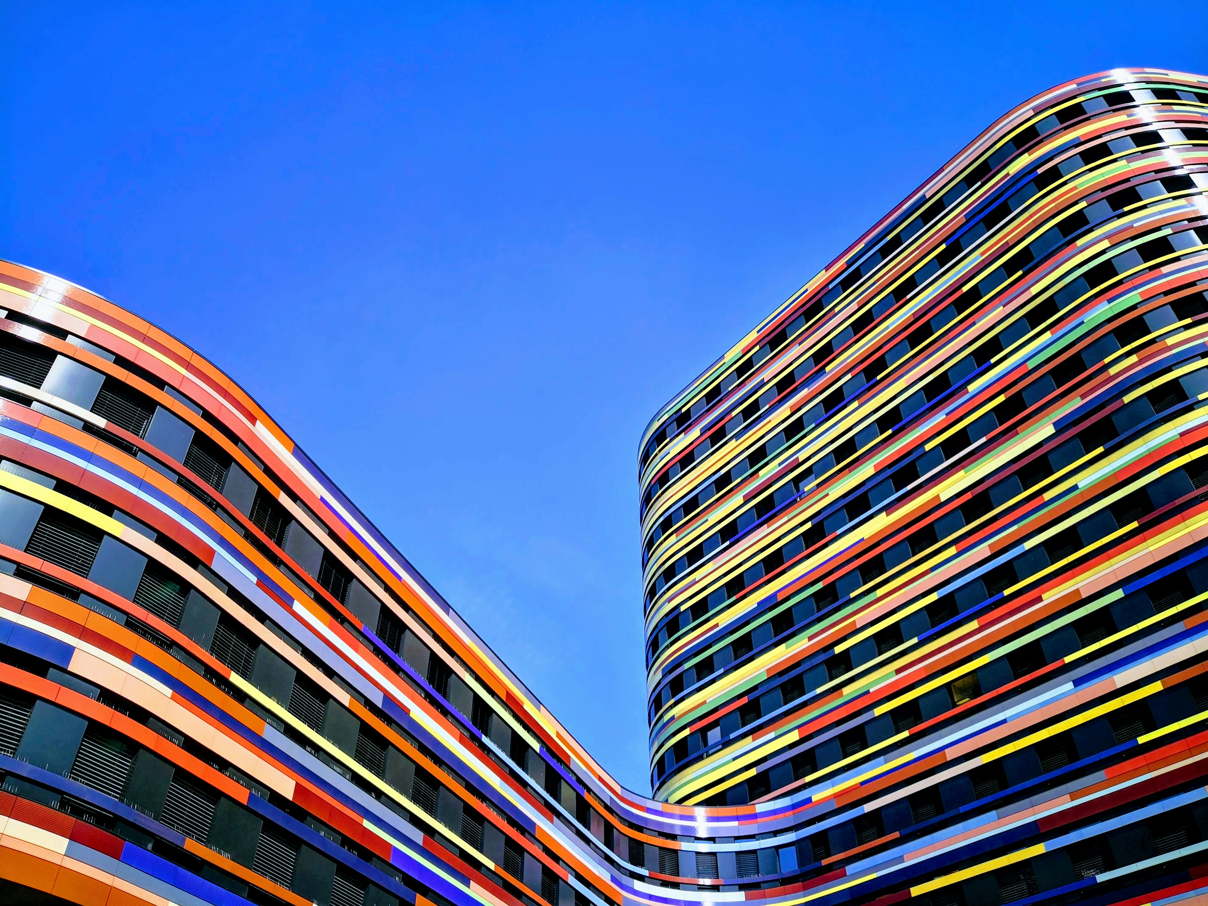 Colorful modern building facades curve into each other against a bright blue sky, forming a dynamic architectural composition.