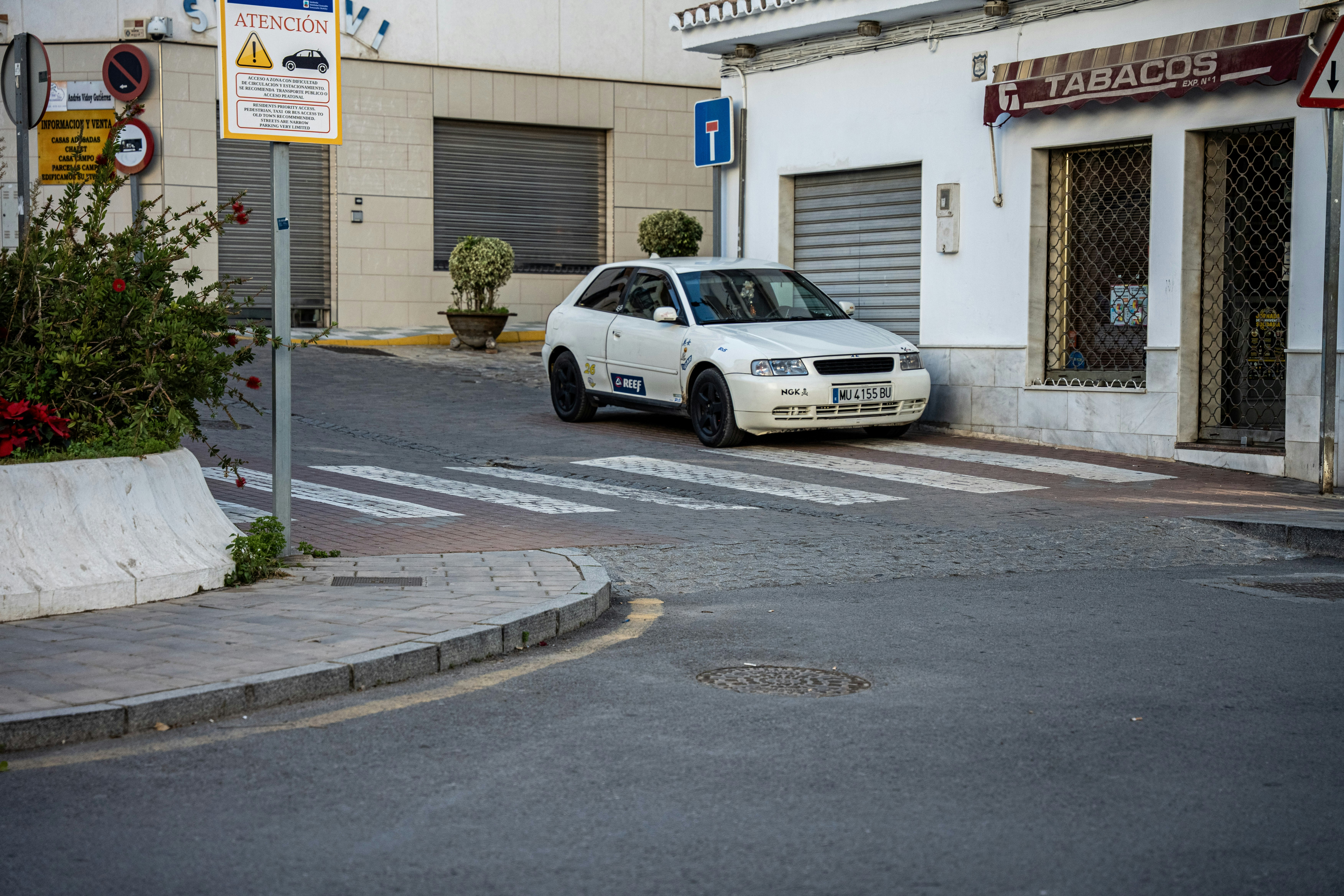 White Sedan Pauses at a Sunlit Spanish Street Corner