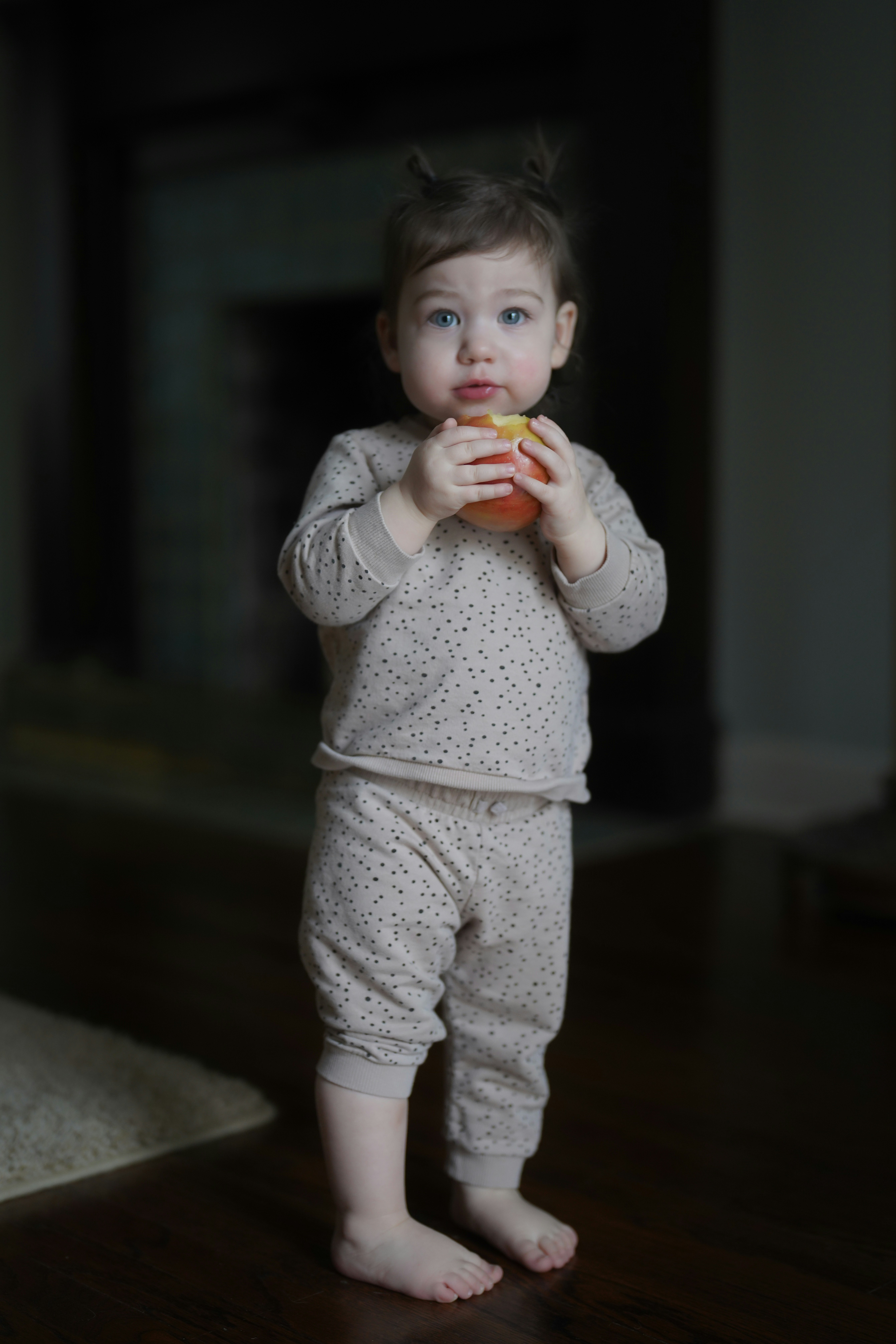 First Orchard Moment: A toddler clutching a sun-warmed fruit in a dim living room.
