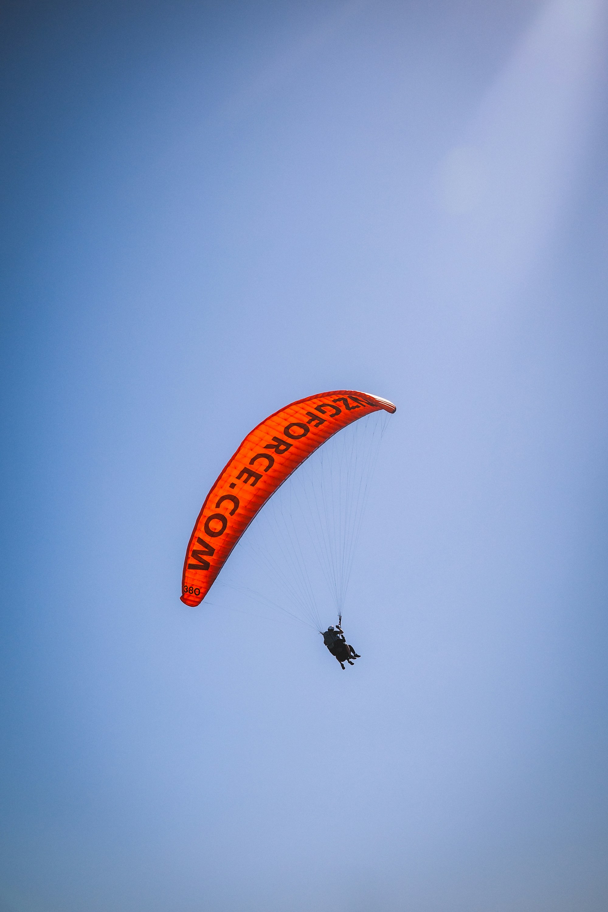 Orange paraglider arcs across a clear blue expanse