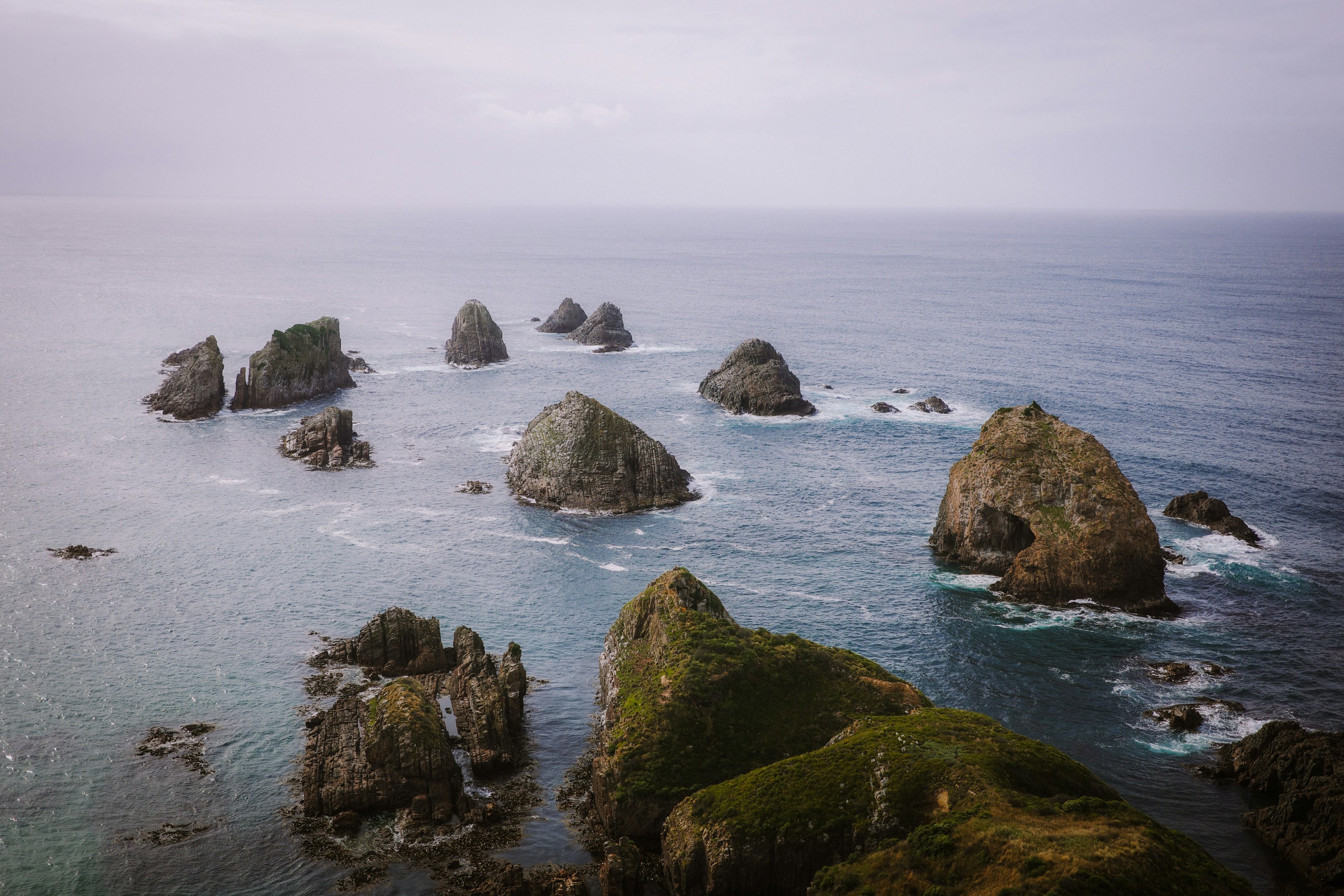 Rocky sea stacks rise from the ocean under a cloudy sky.