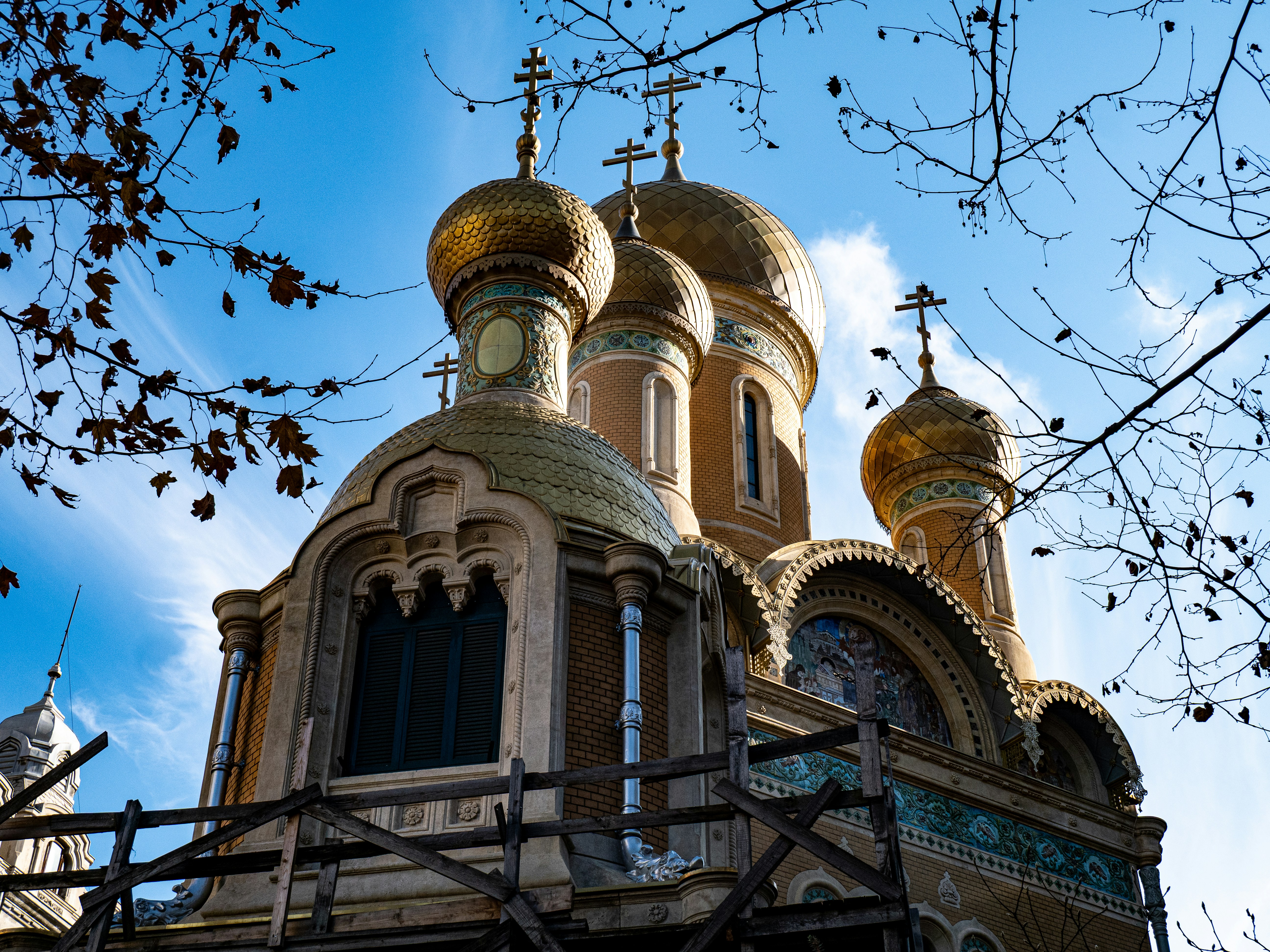 Ornate church domes glistening in sunlight, framed by bare tree branches against a vivid blue sky.