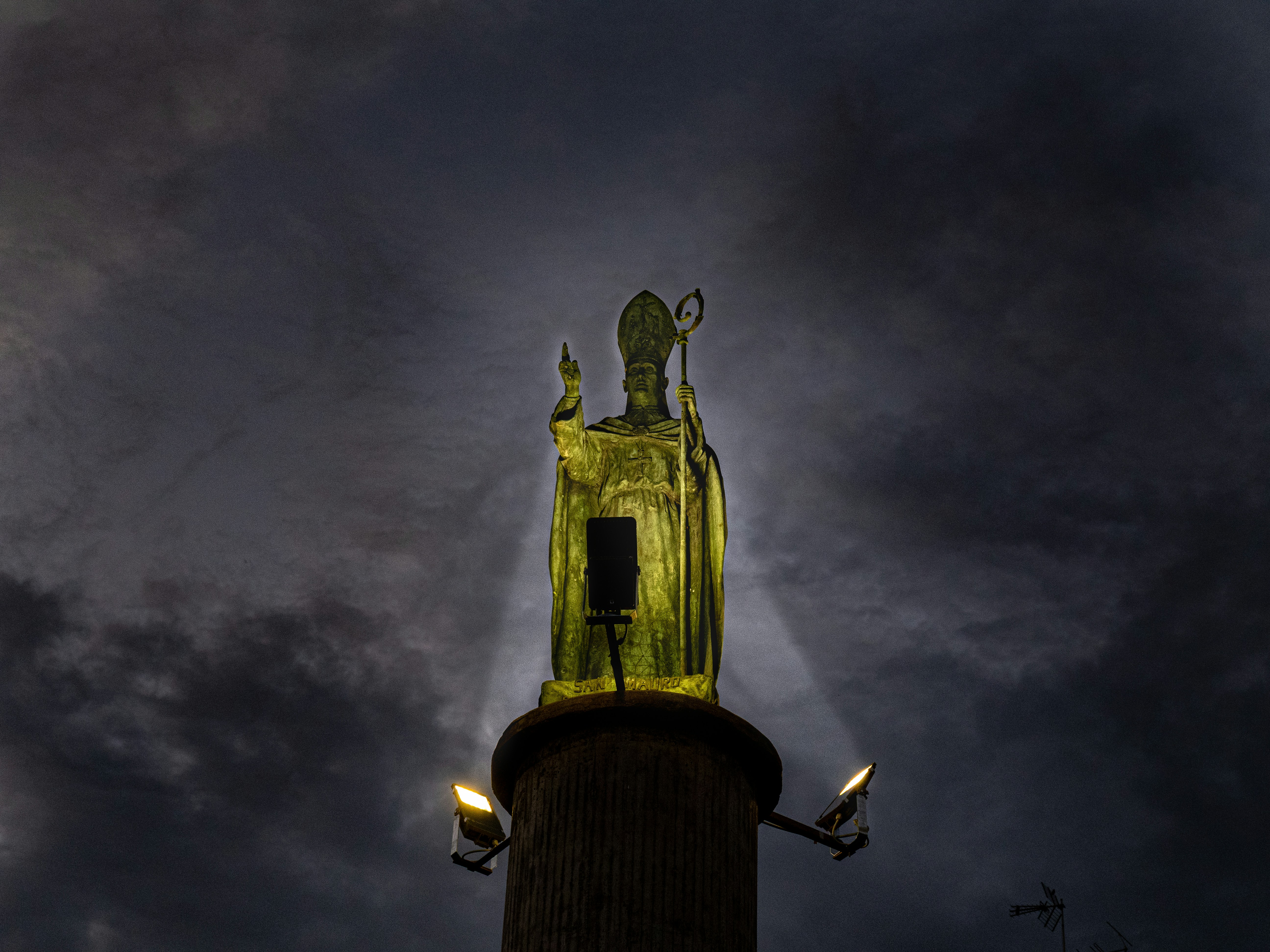 Illuminated statue atop a column against a dramatic cloudy night sky.