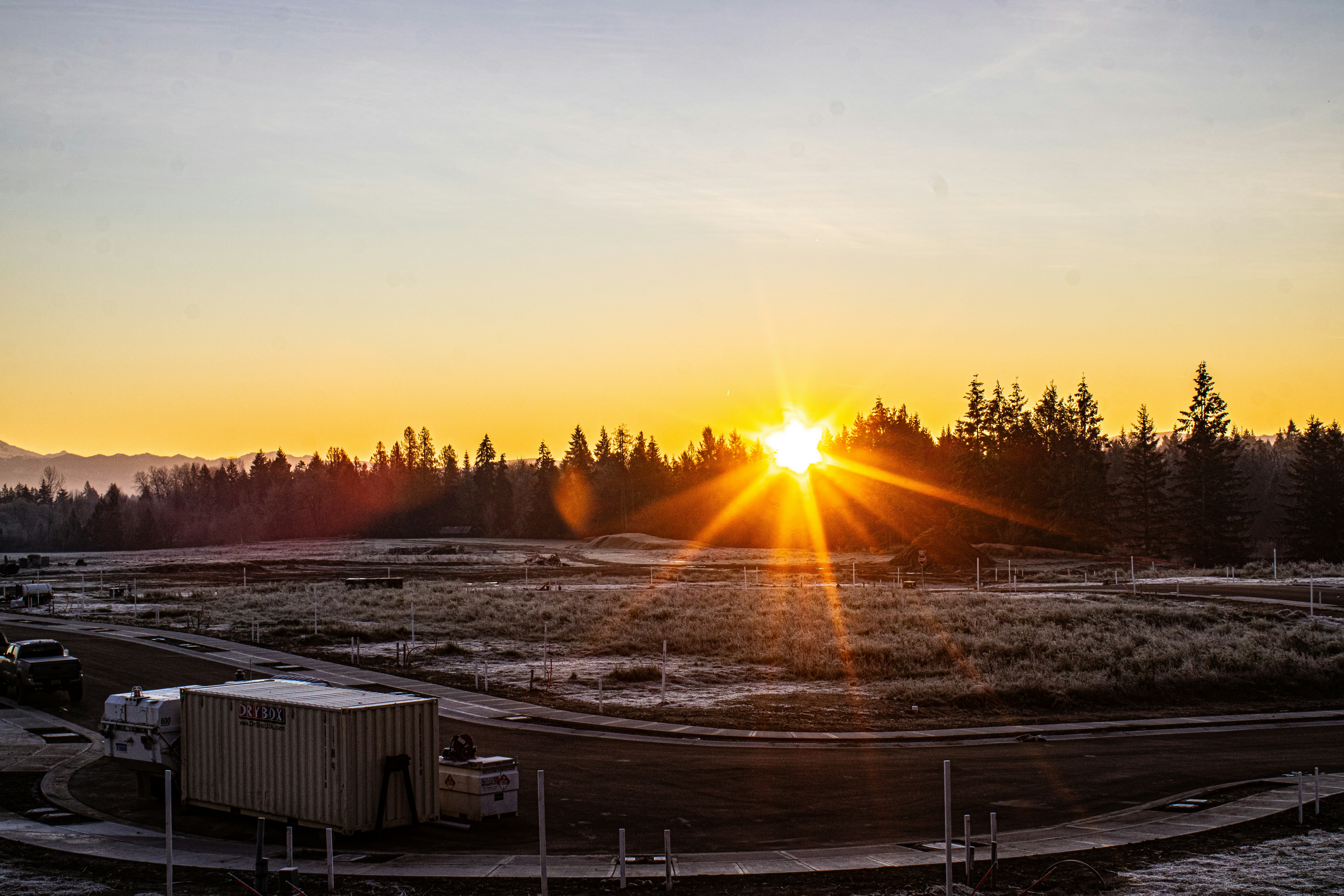 Sunrise casting golden light over a frosted landscape with silhouetted trees and distant mountains.
