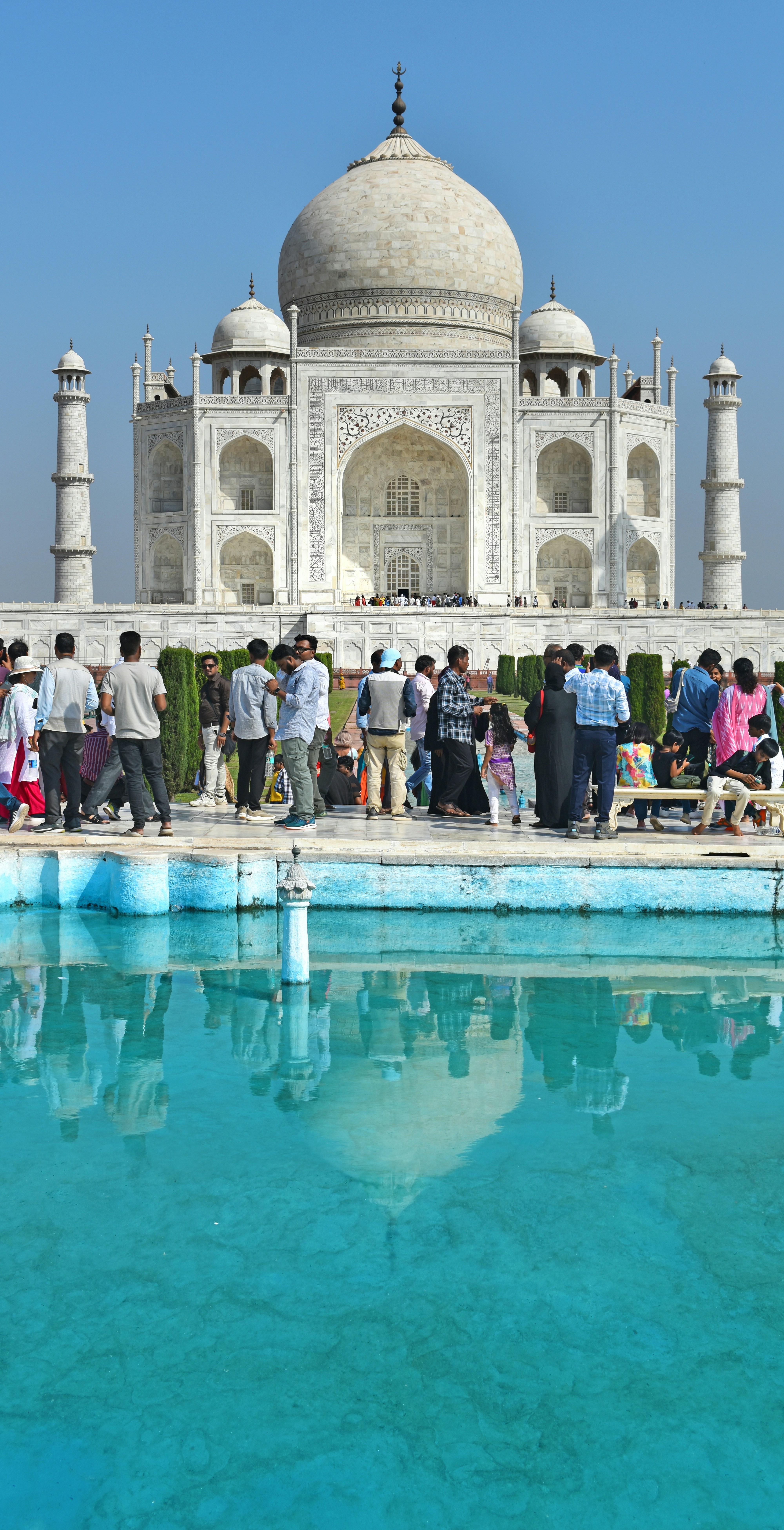 Taj Mahal partially reflected in a turquoise pool with a group of visitors in the foreground.