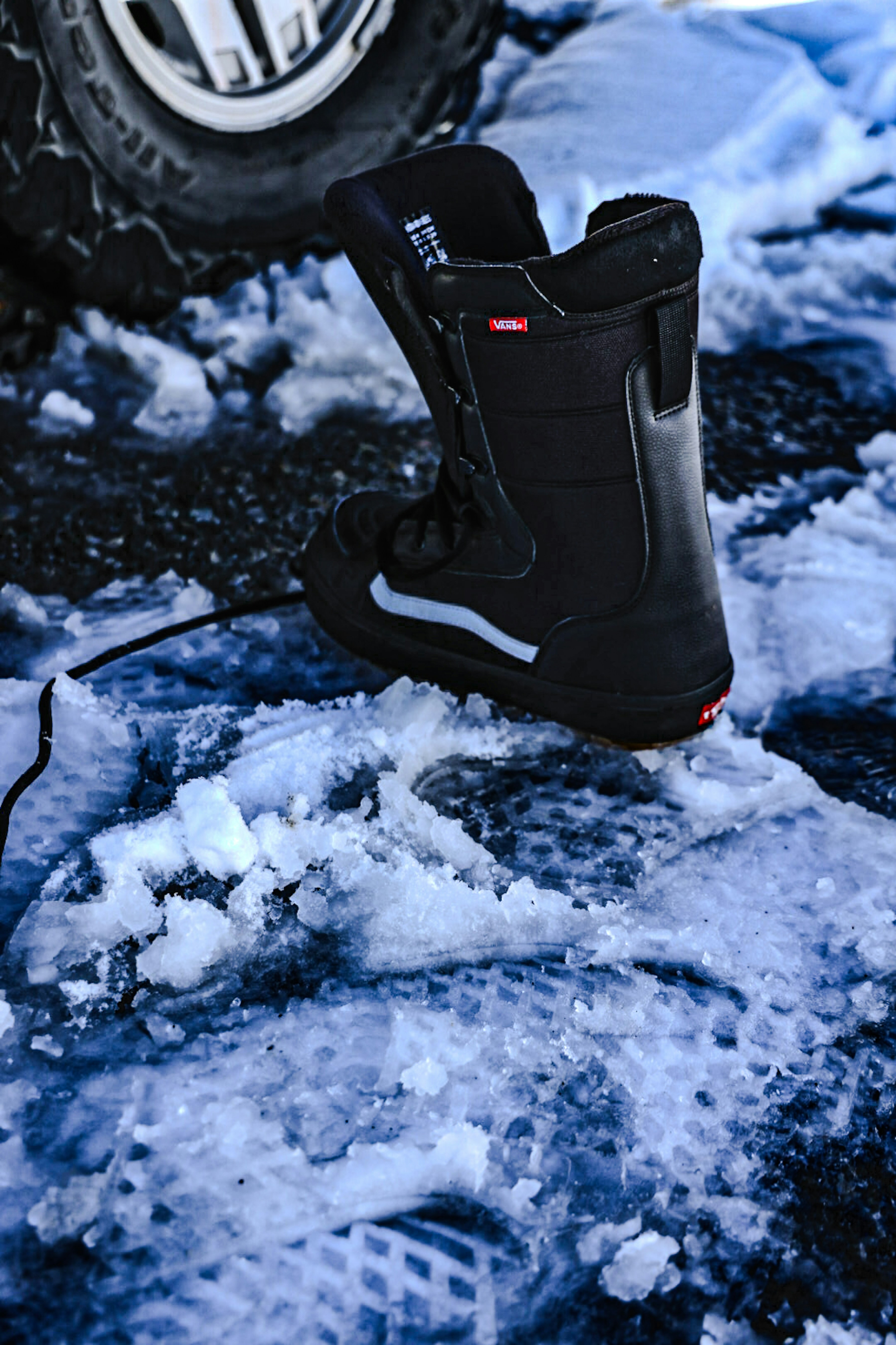 Lone snowboard boot on cobalt ice, tire shadow in the cold