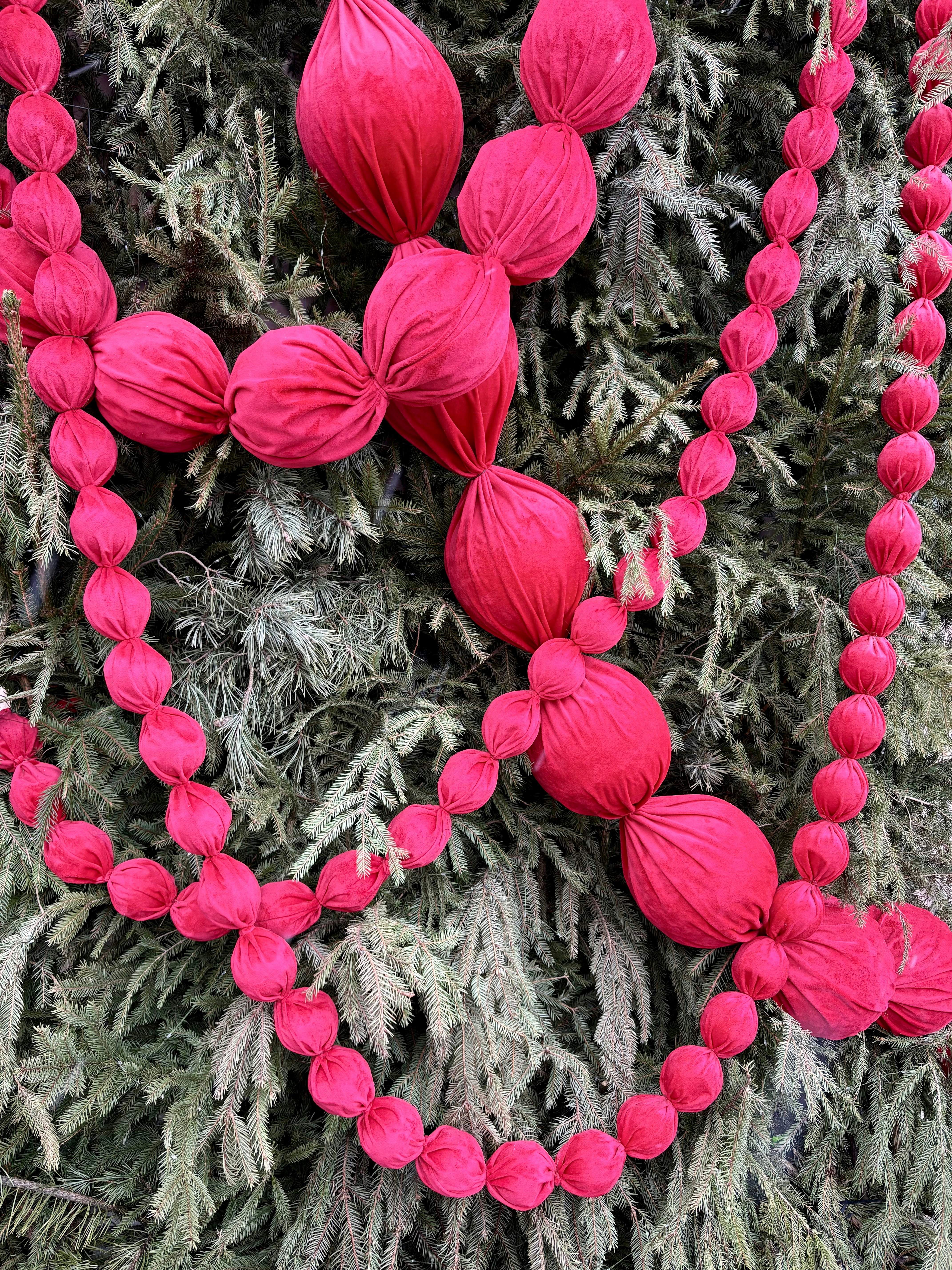 Bright magenta bead garlands loop across frosted evergreen branches, creating a festive, textural holiday scene.