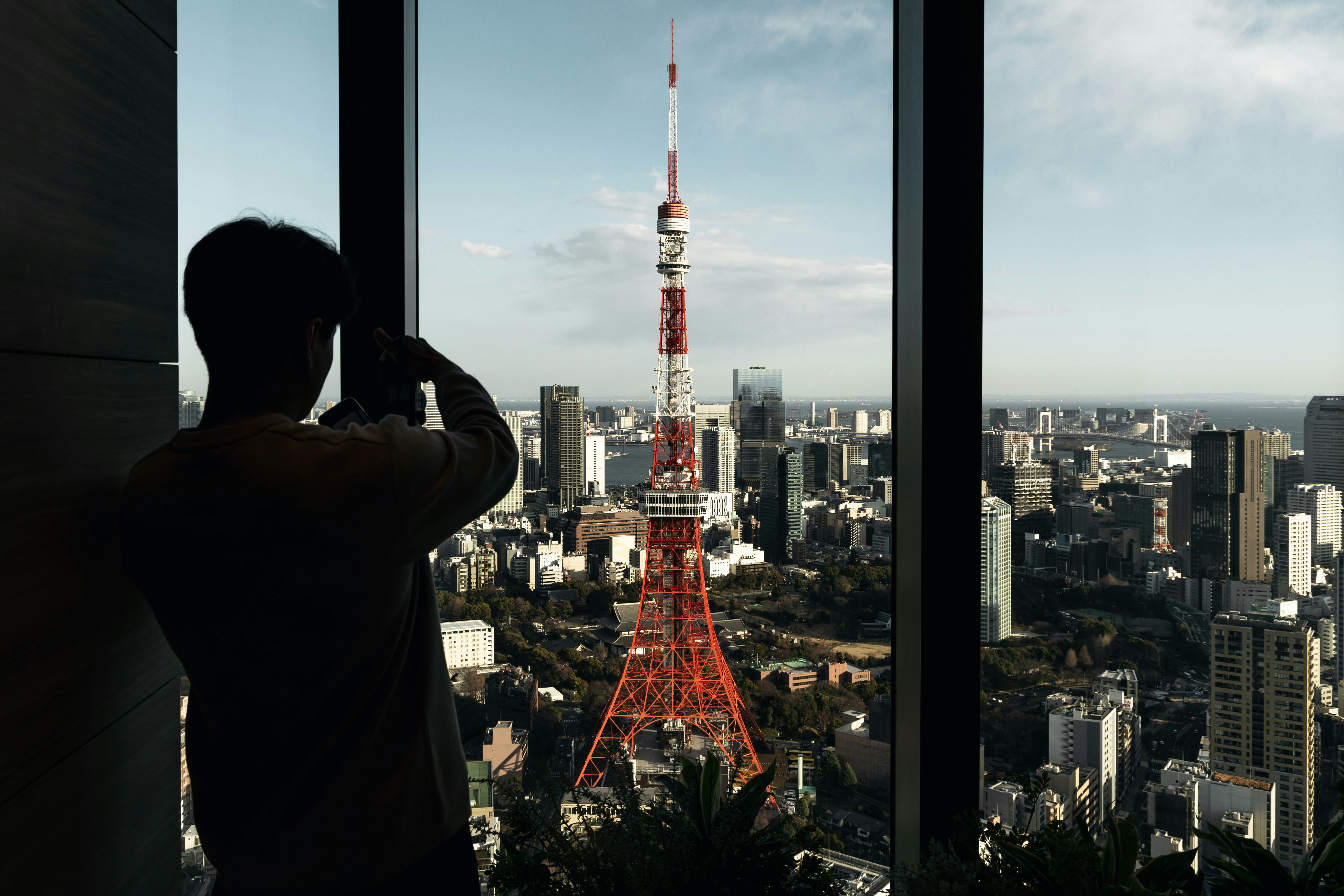 Silhouette of a person photographing Tokyo Tower through a window overlooking the cityscape.