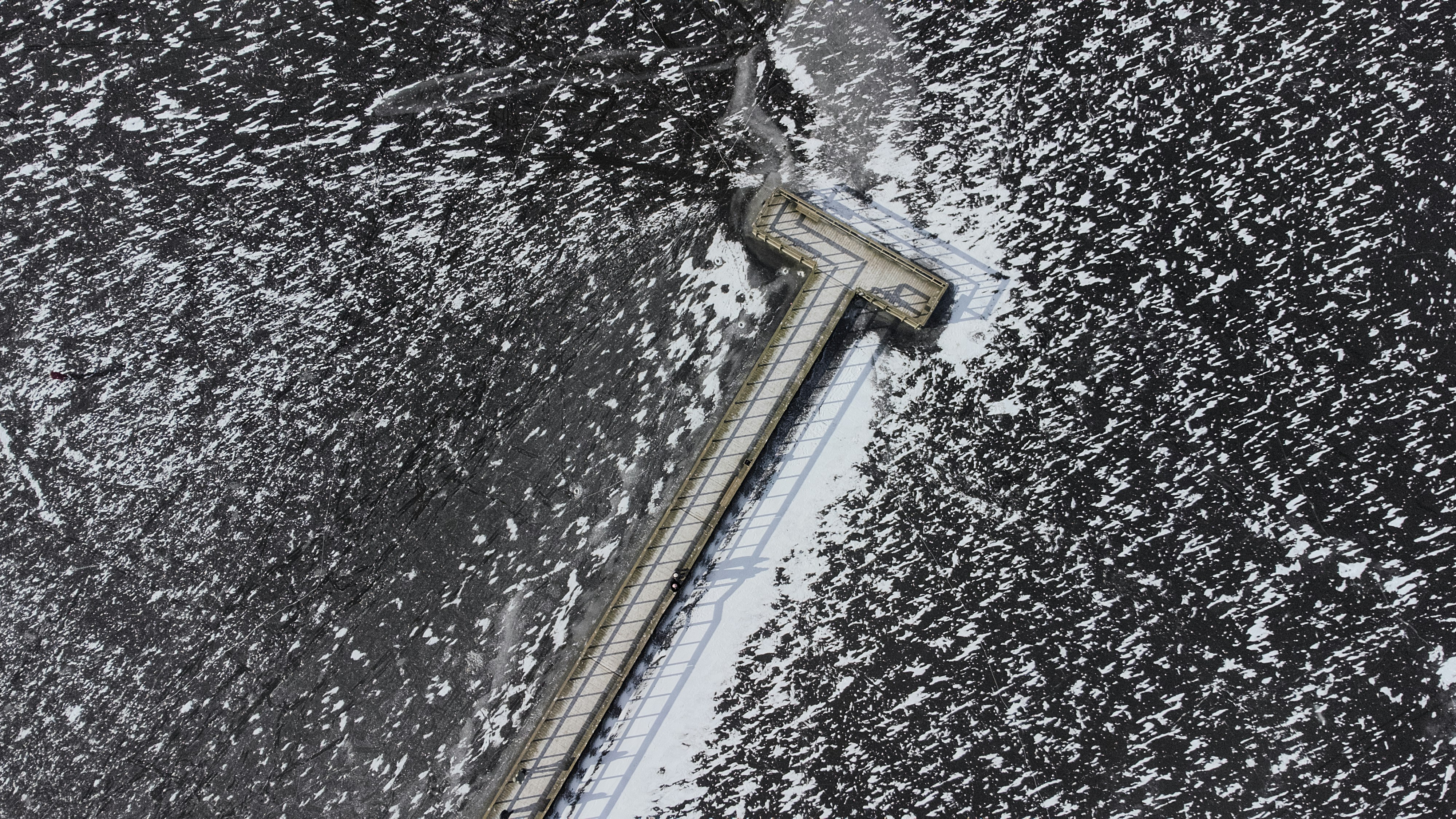 Aerial view of a snow-dusted pier extending over the frozen surface of Lake Rekyva.