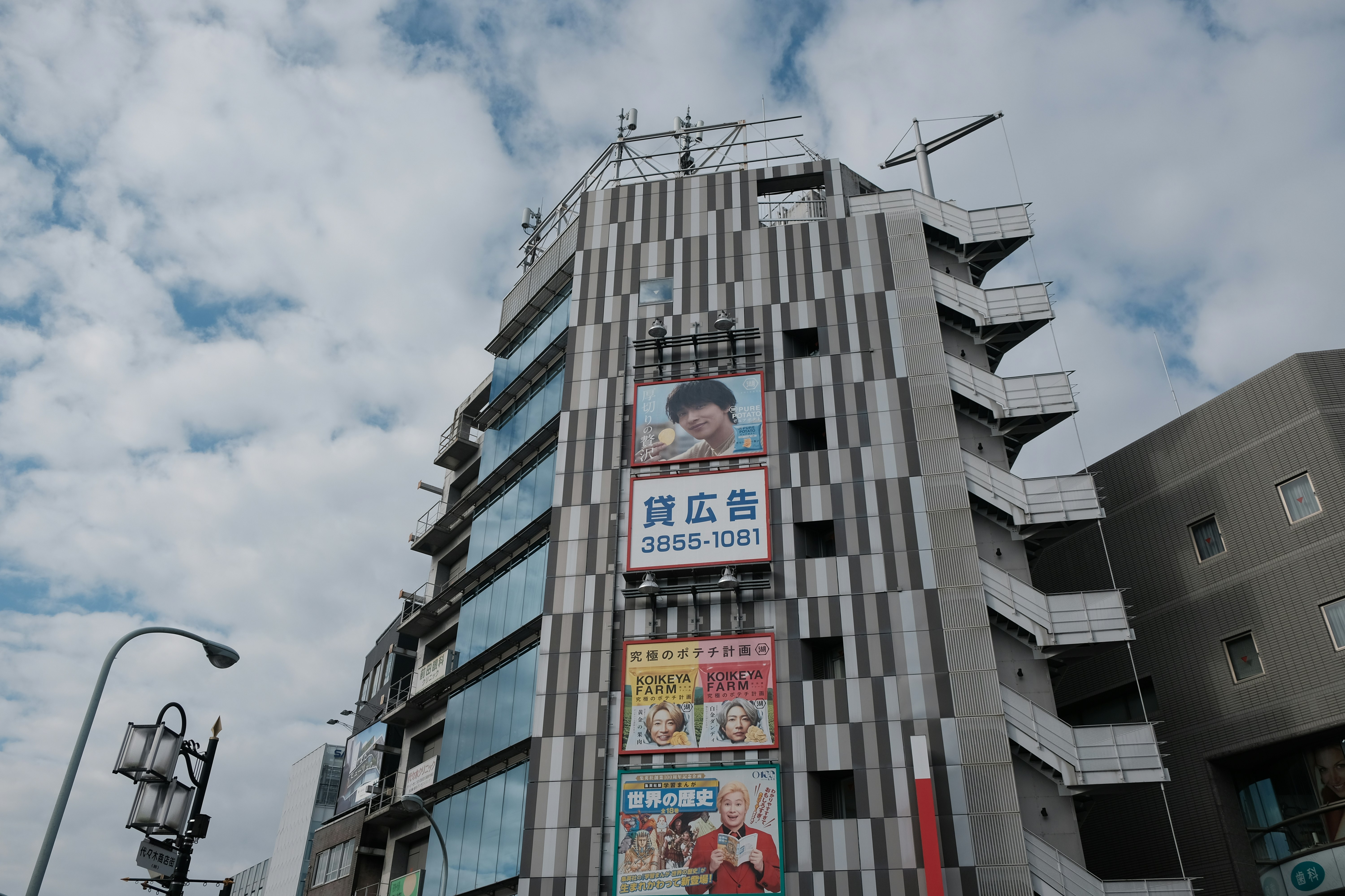 Modern building facade with geometric patterns and various colorful advertisements under a cloudy sky.