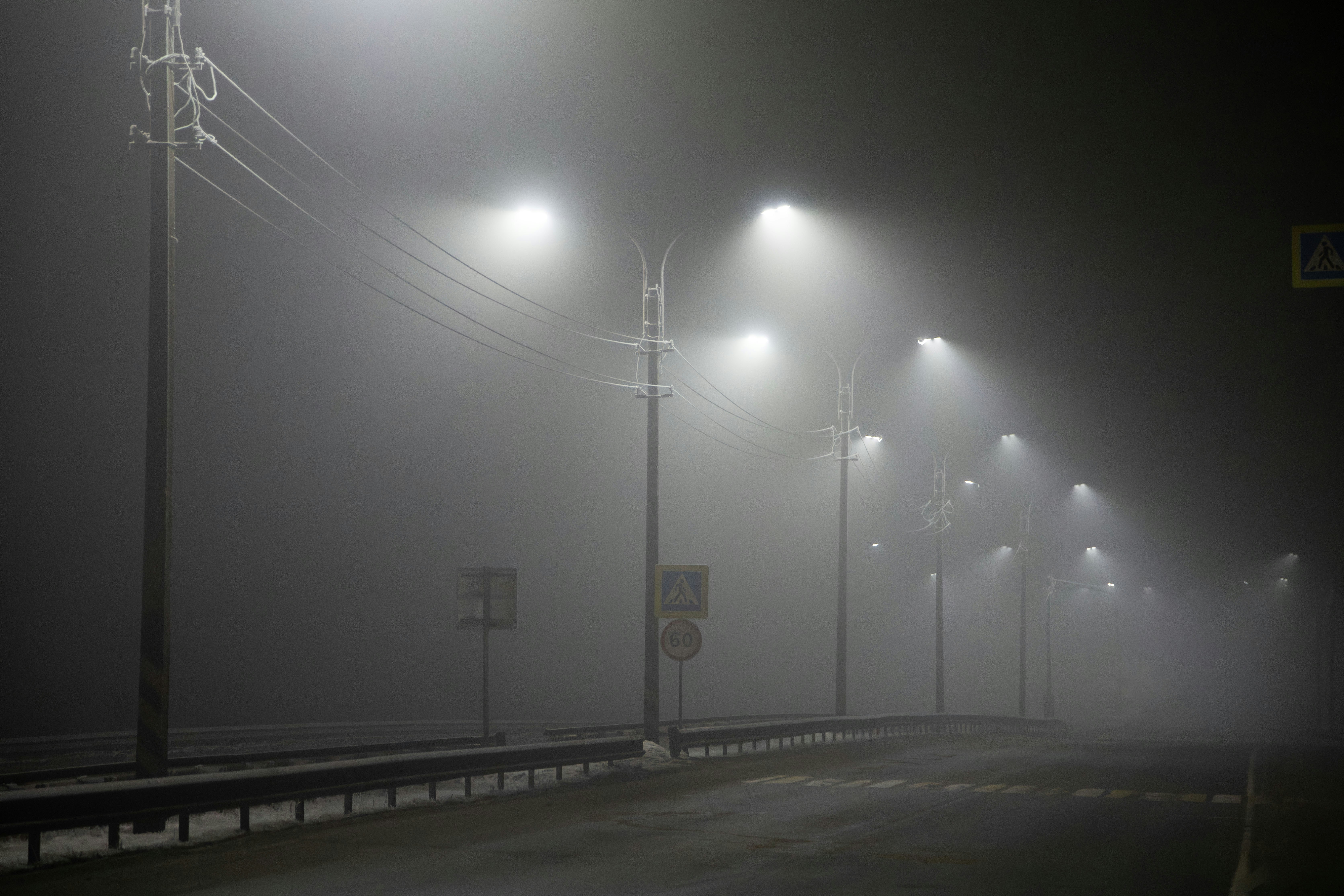 Streetlights cast a soft glow over a deserted road enveloped in dense fog.