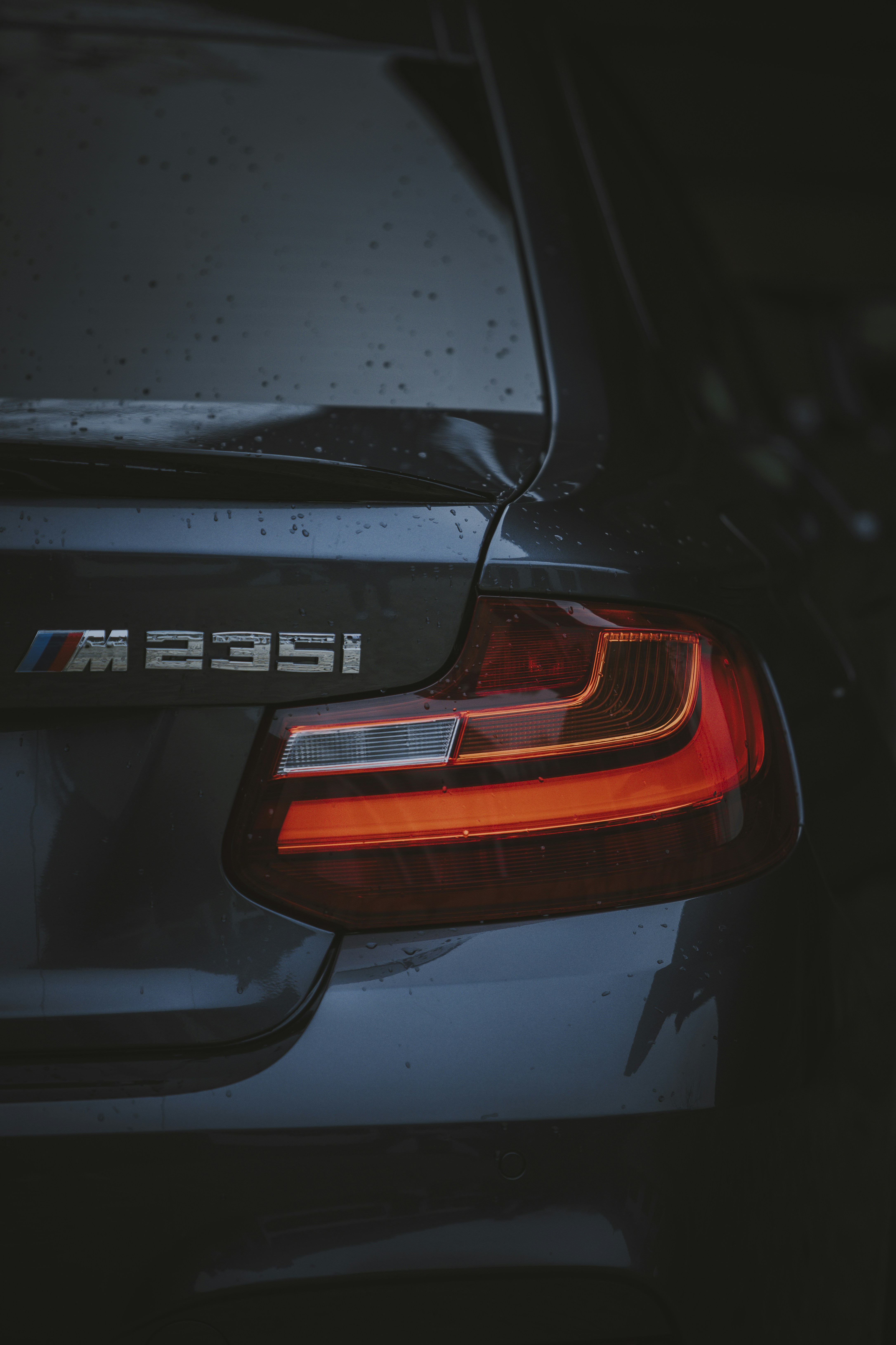 Crimson Arc: Rain-speckled BMW M235i Tail Light in Low Light