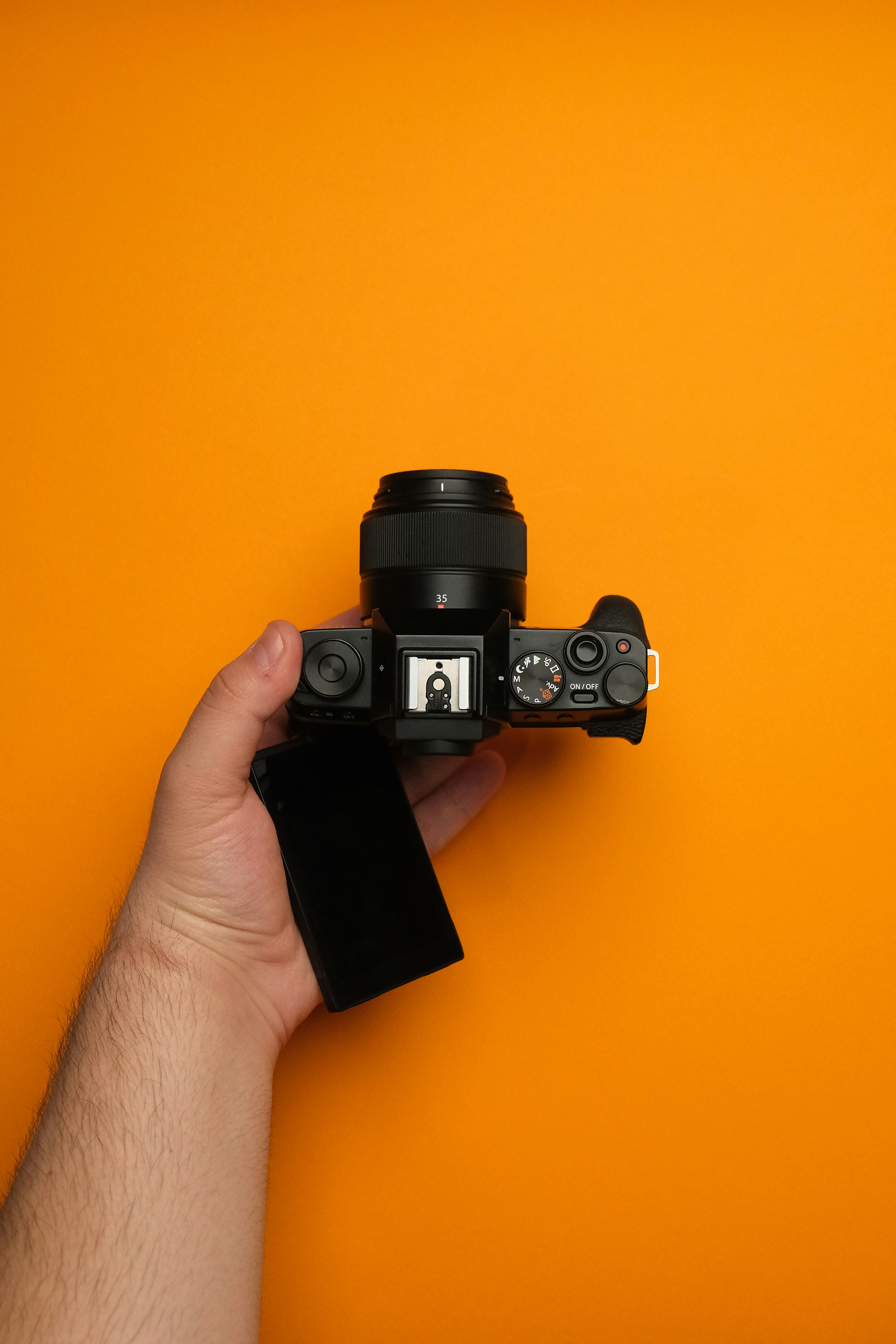 Top-Down Snapshot: A Hand-Held Mirrorless Camera on a Vibrant Orange Backdrop