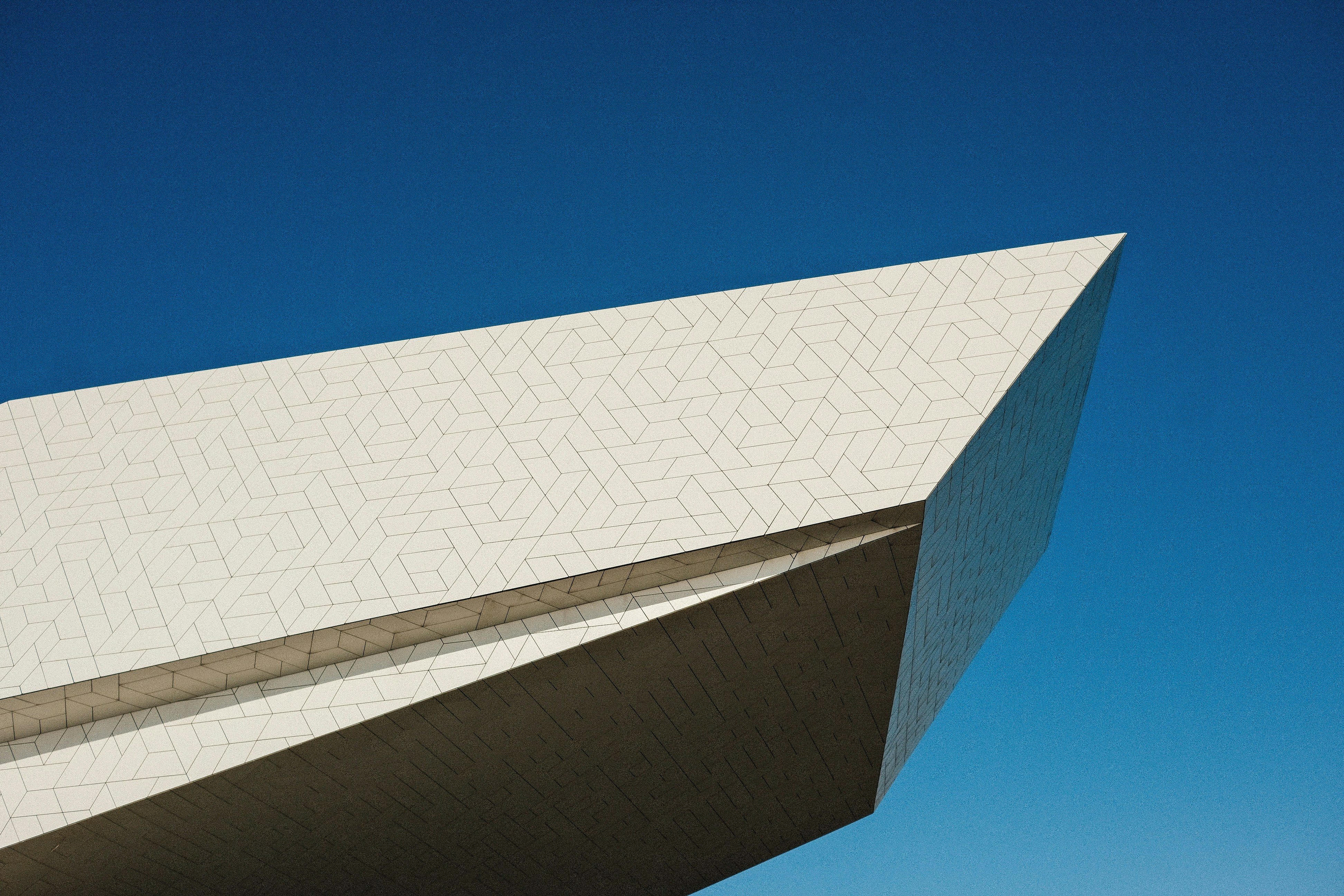 Abstract architectural structure with textured white surface against a clear blue sky.
