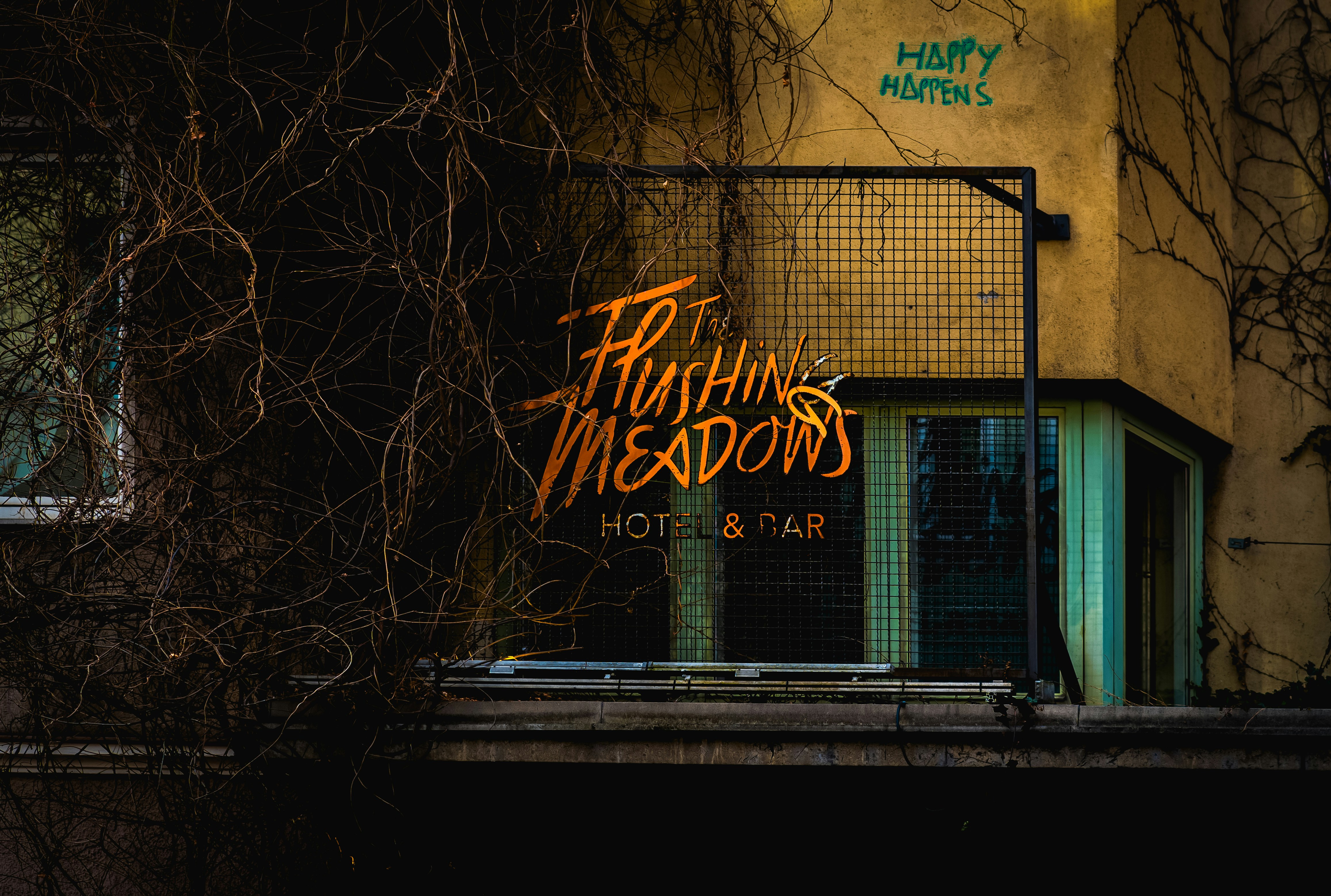 Vines cover the facade of a building with a neon hotel sign and street art.