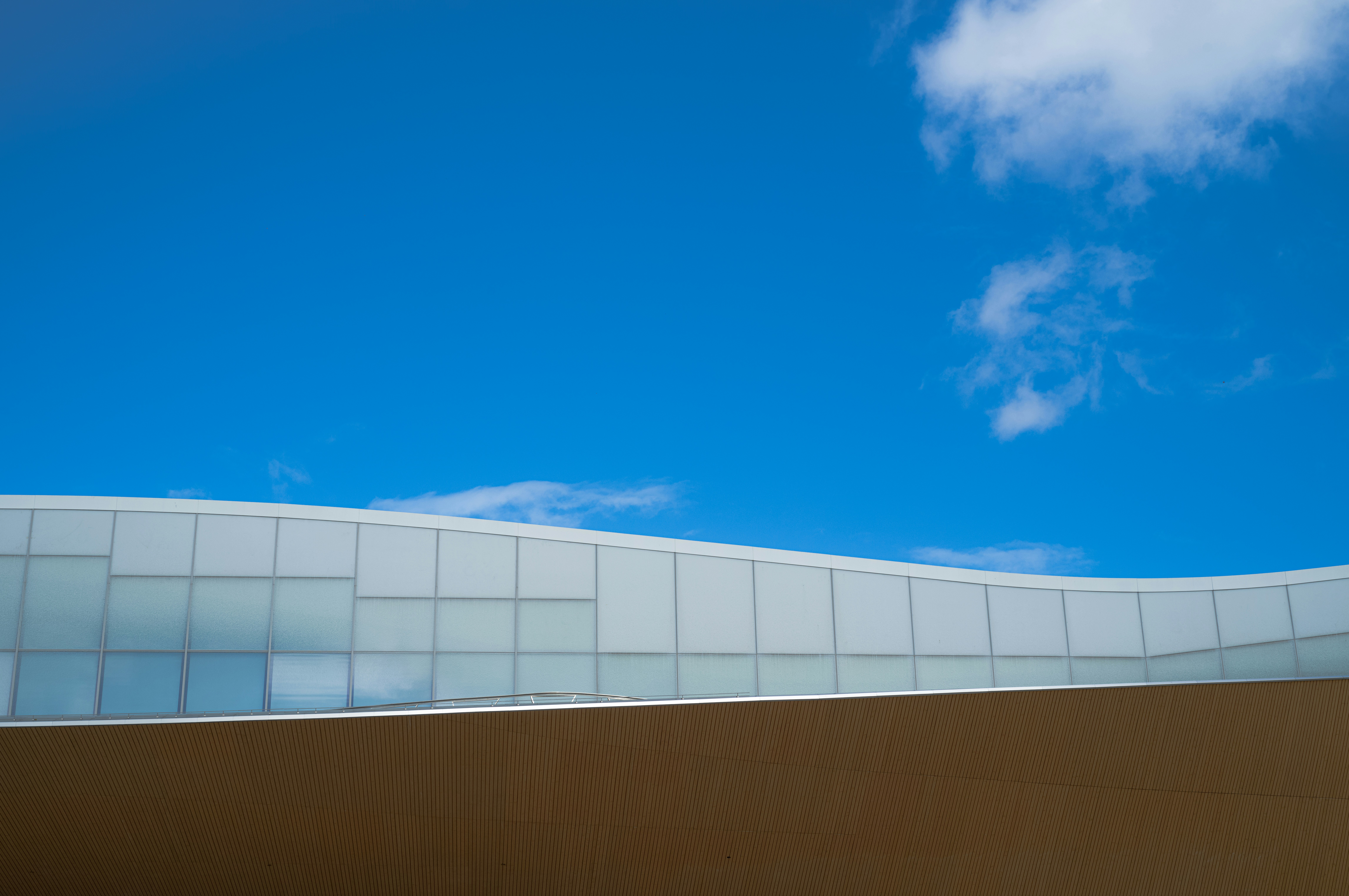 Modern architectural facade with a wavy design set against a bright blue sky with scattered clouds.