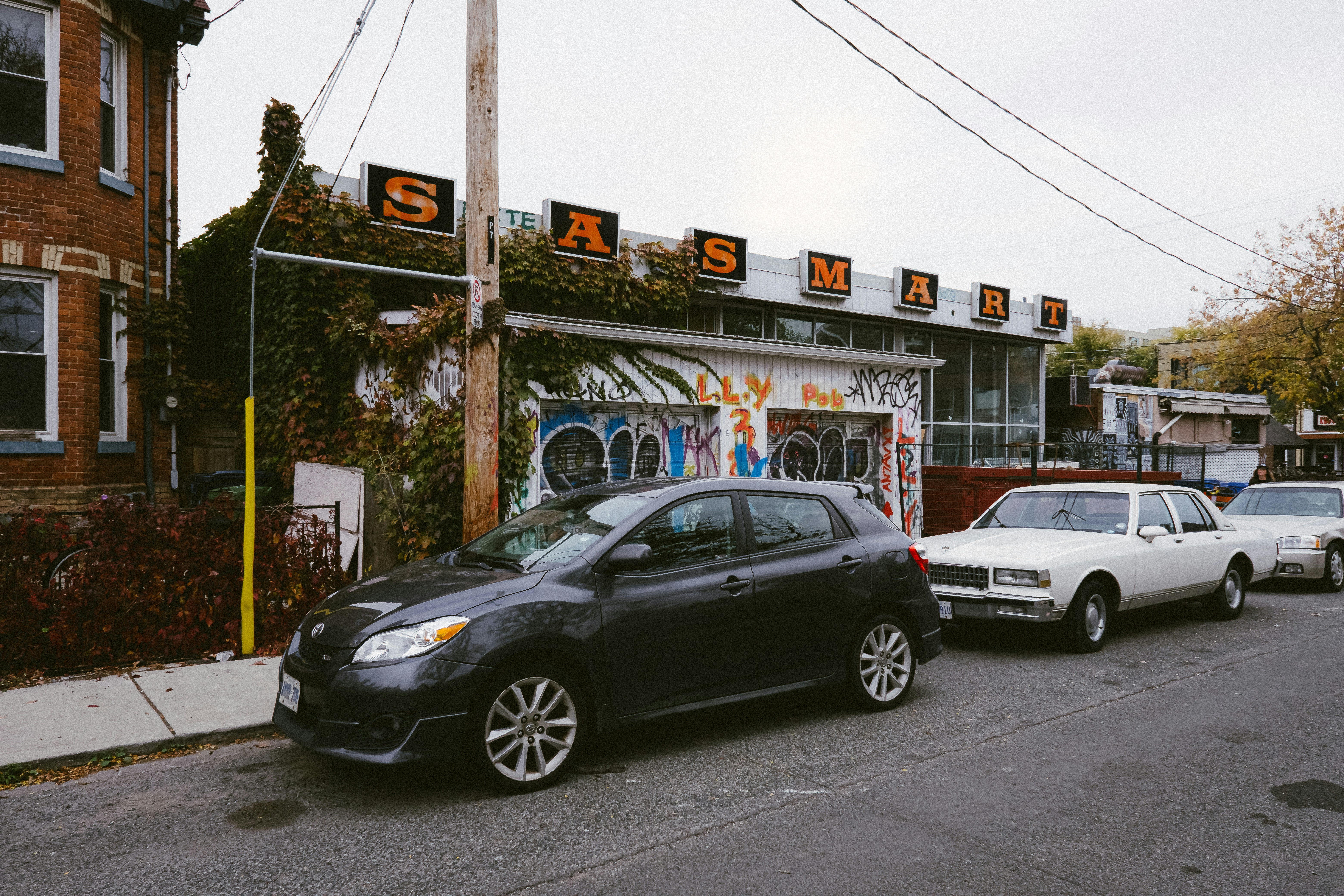 Black Hatchback Anchors a Graffiti-Splashed Street in Front of a Neighborhood Market