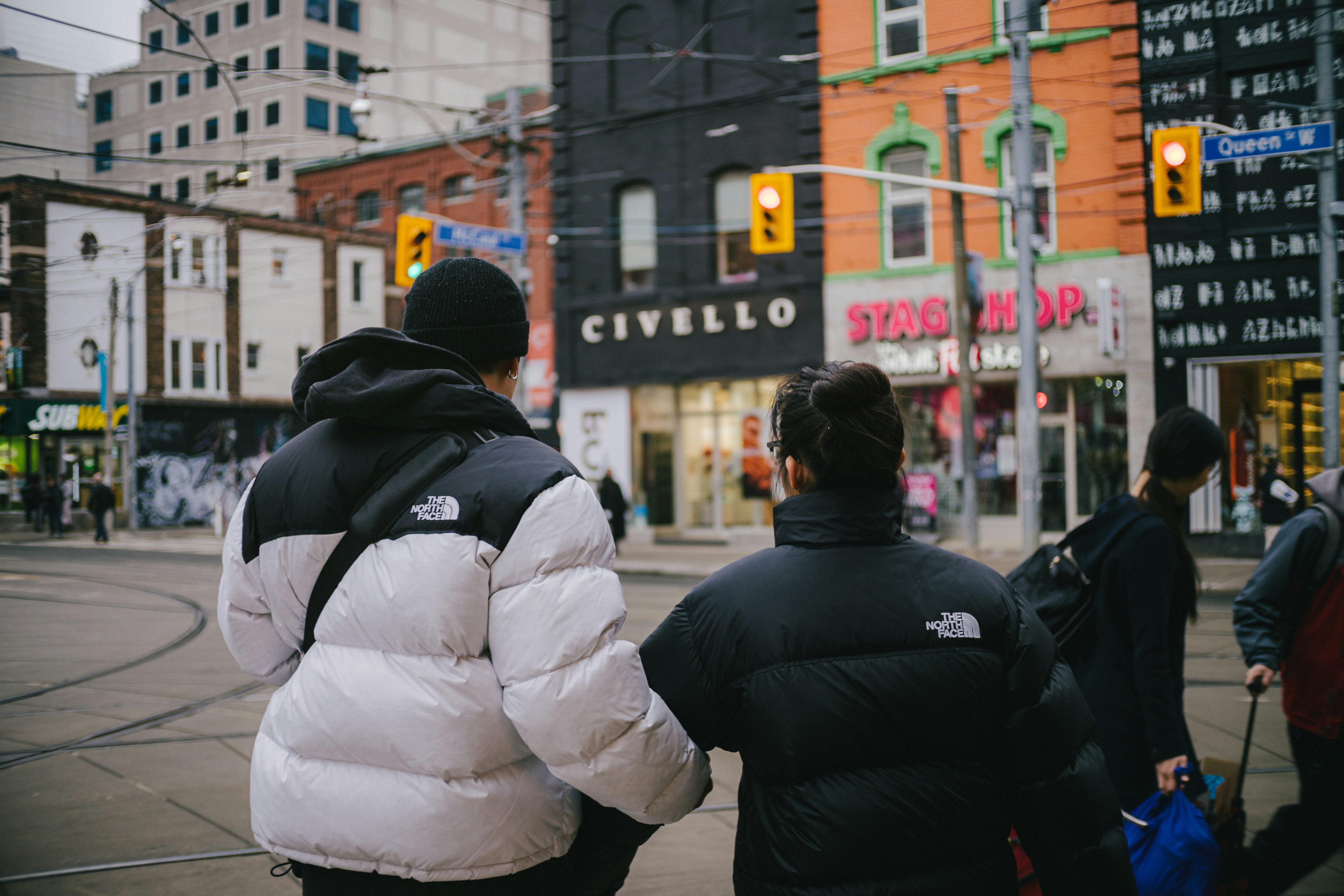 Coats in the City: Two Silhouettes Amid Neon Storefronts