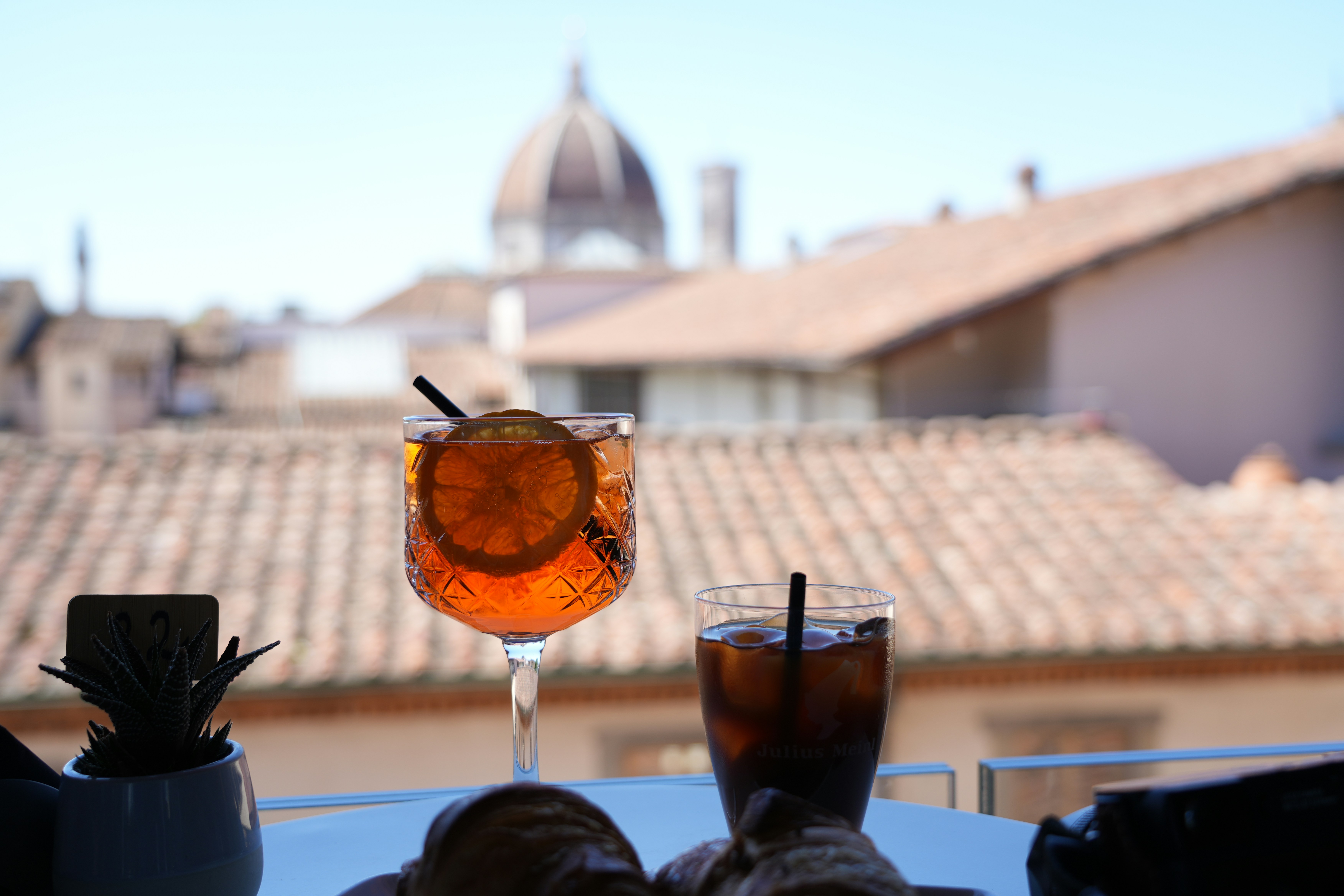 Cocktails on a table with a Tuscan rooftop view under a clear sky.