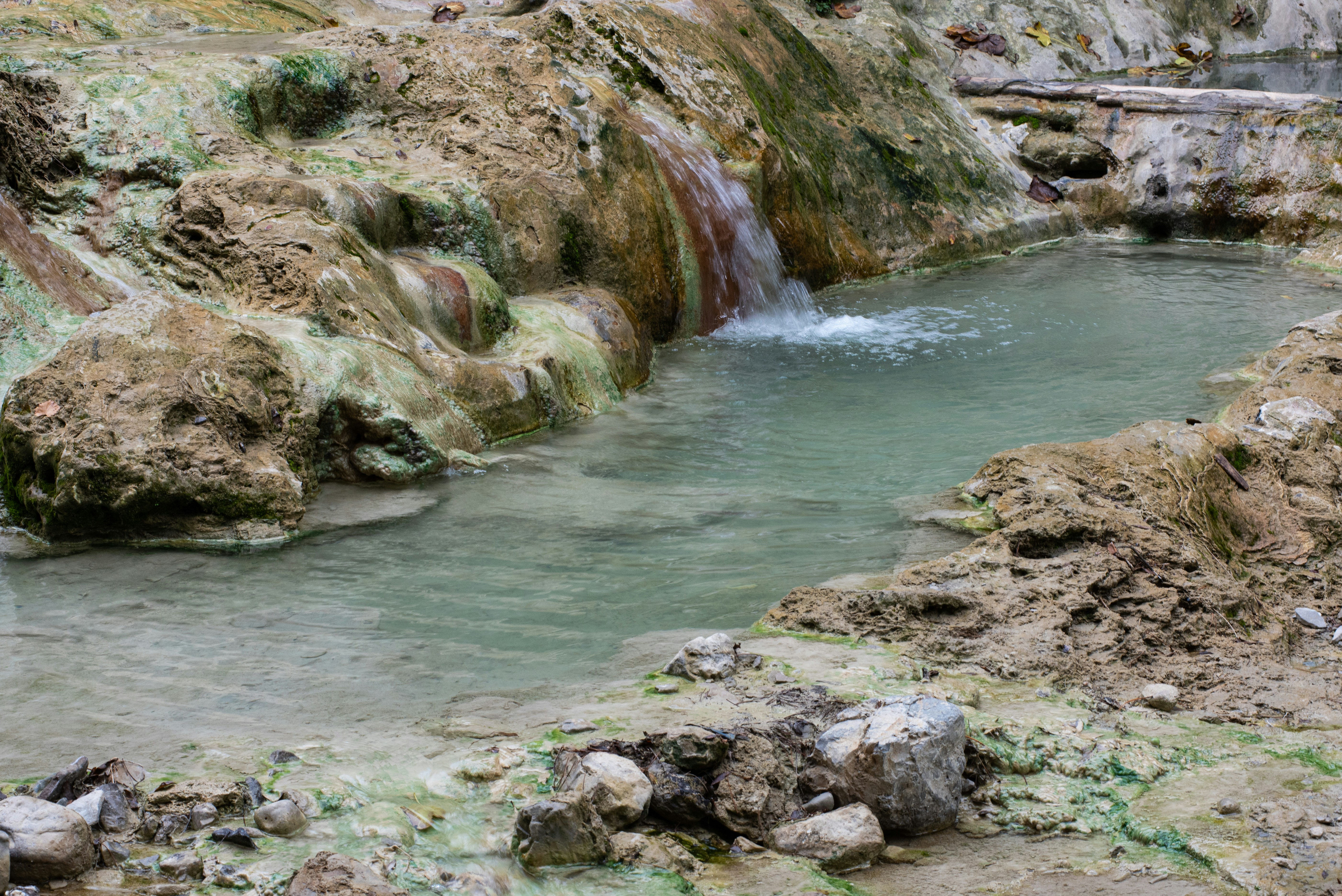 Natural pool formed by a gentle waterfall amid rocky terrain.