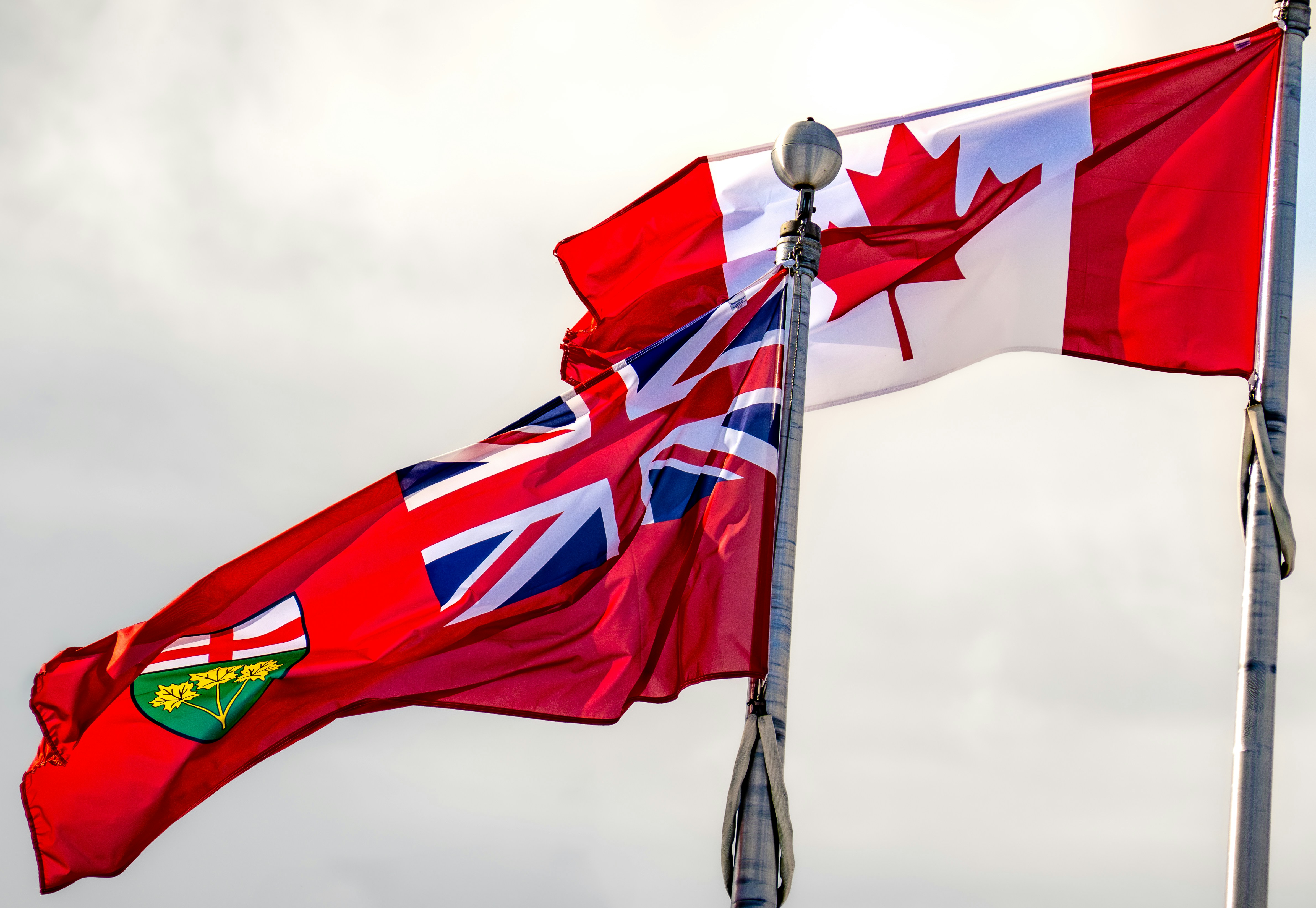 Canadian and Ontario flags waving against a cloudy sky.