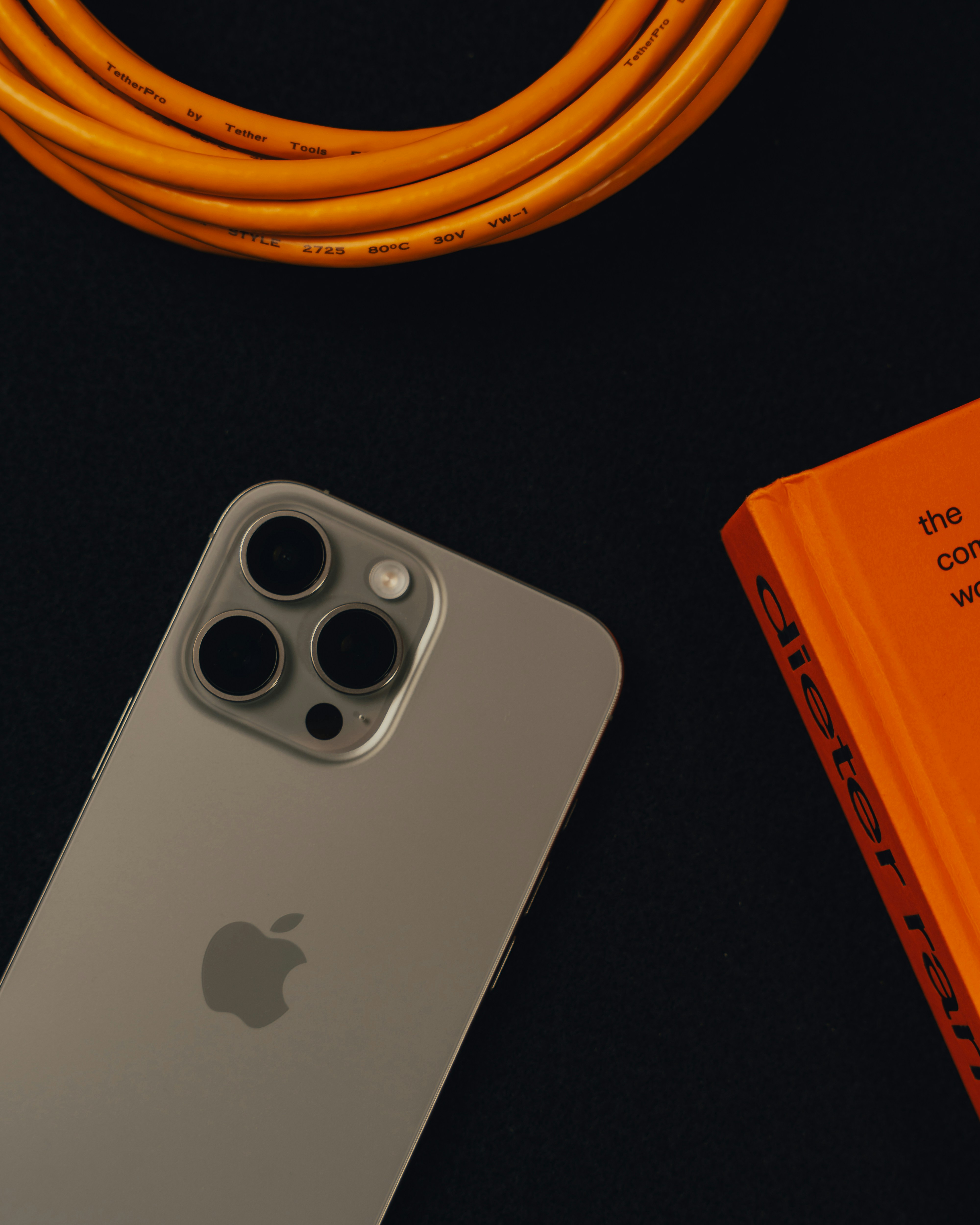 Quad-Camera Focus: iPhone, Orange Coil, and a Bold Orange Book