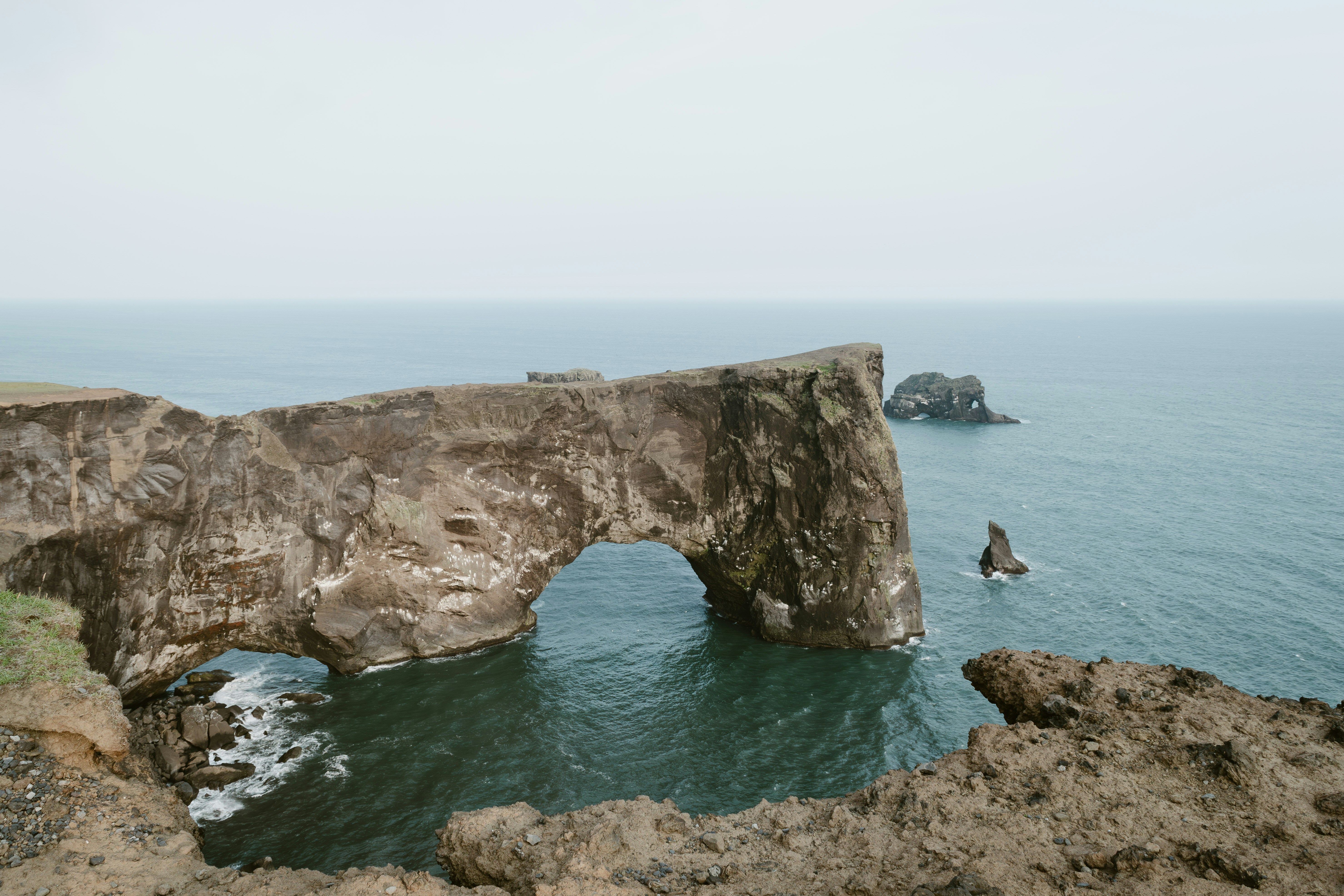 Natural rock arch over turquoise ocean waters with rugged cliffs in the foreground.
