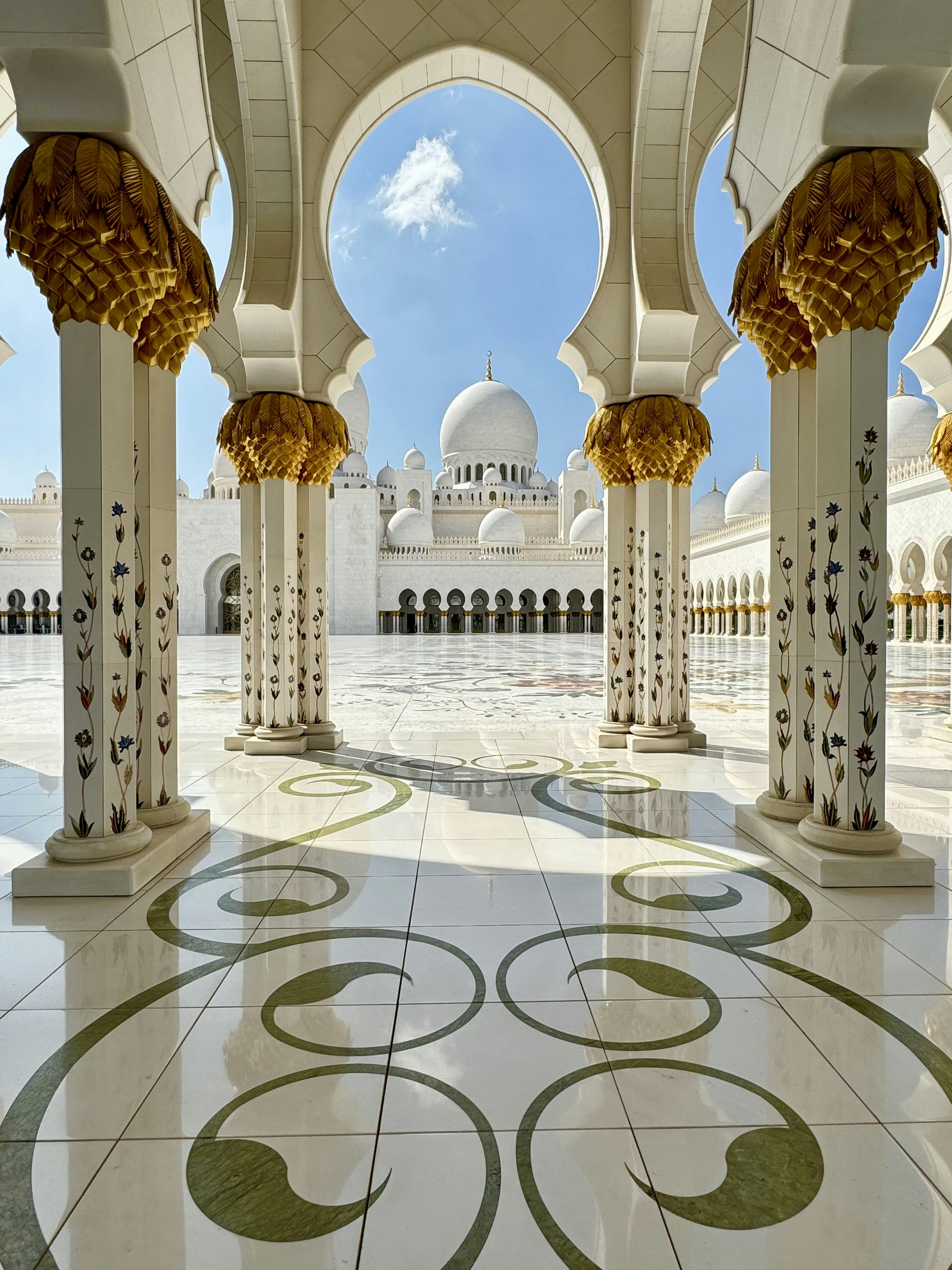 Ornate arches and intricate floor patterns of a grand mosque under a clear blue sky.