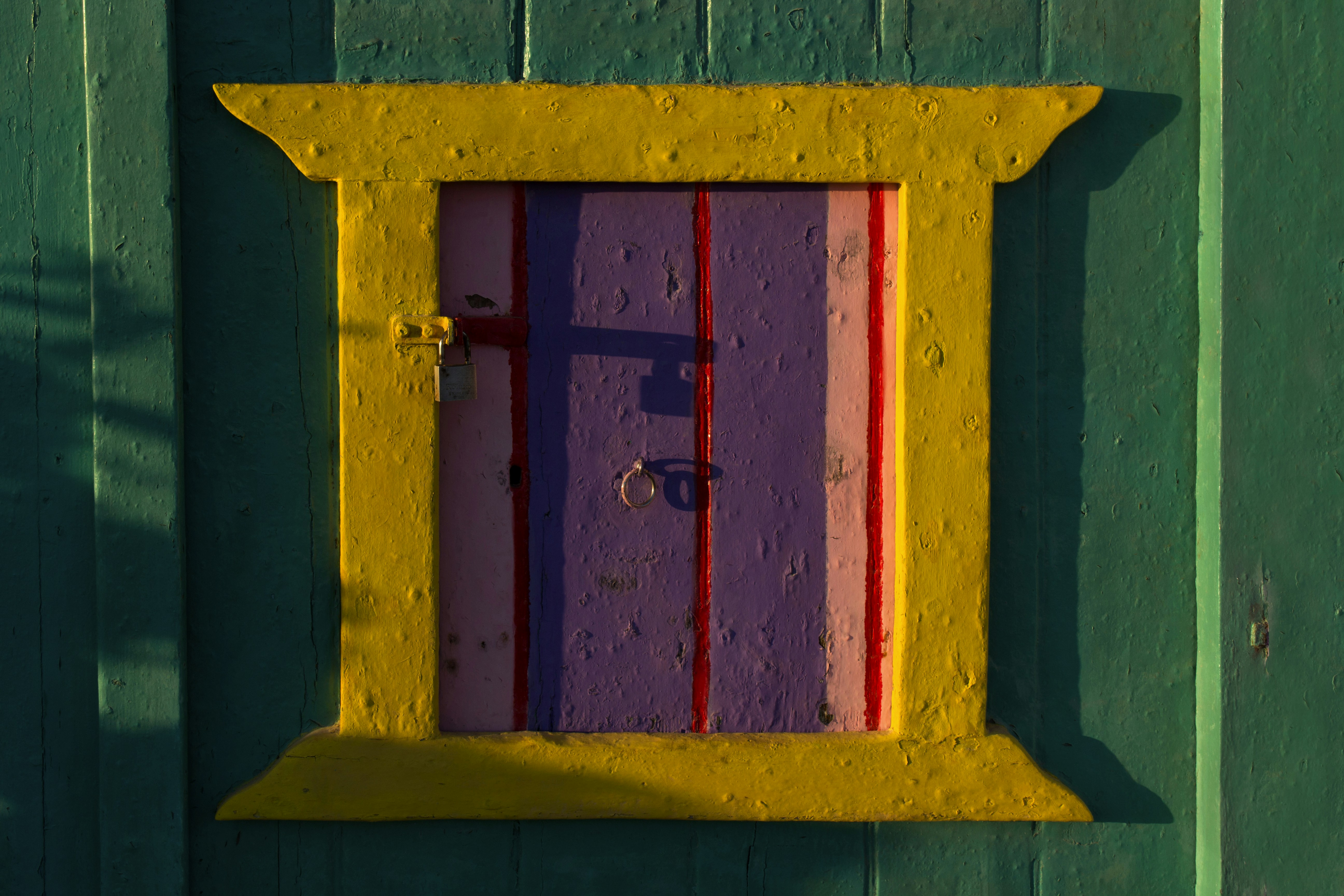 Colorful wooden door with purple panels, framed by yellow, set against a green wall in bright sunlight.
